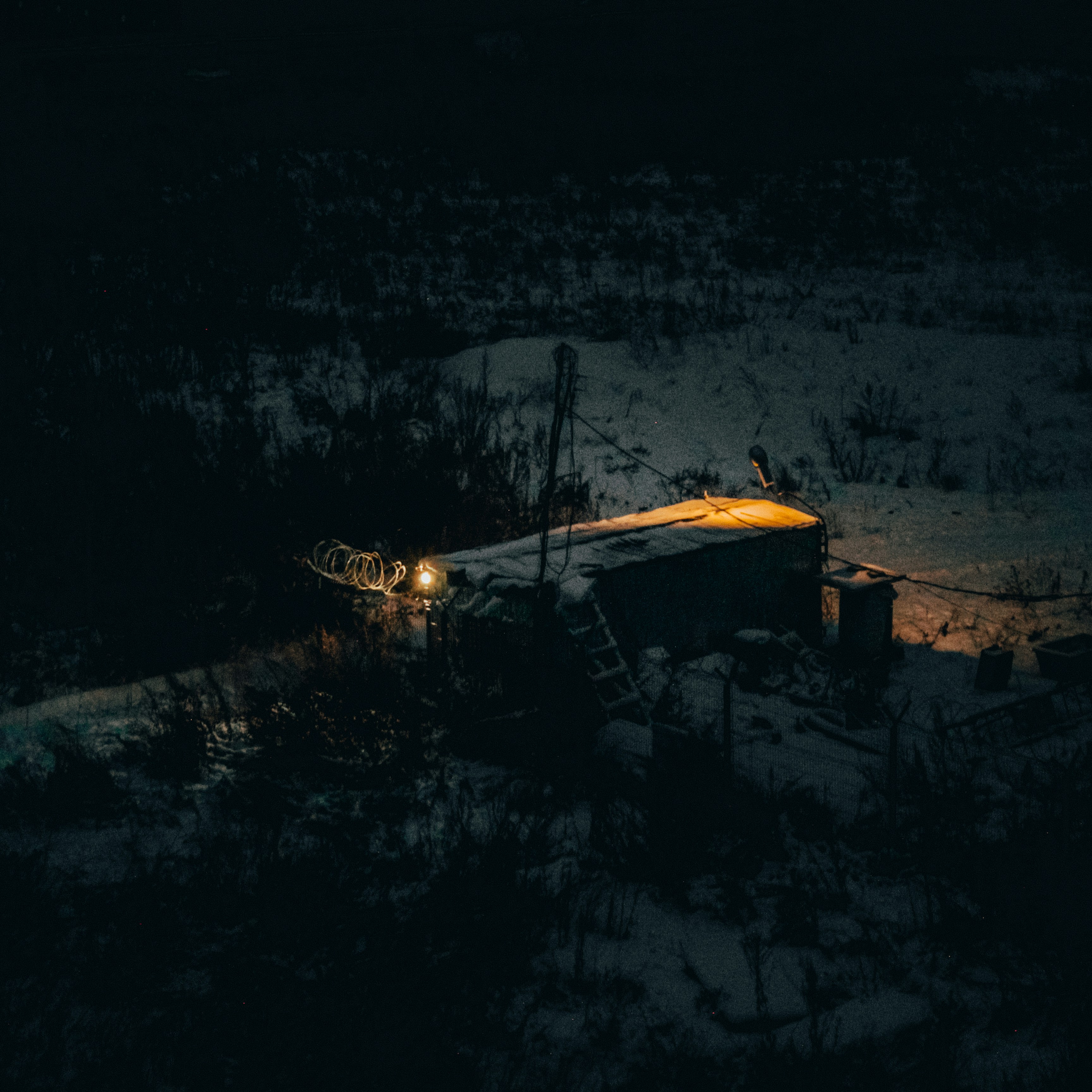 A solitary structure illuminated by a warm light amidst a dark, snowy landscape, evoking a sense of isolation and tranquility.