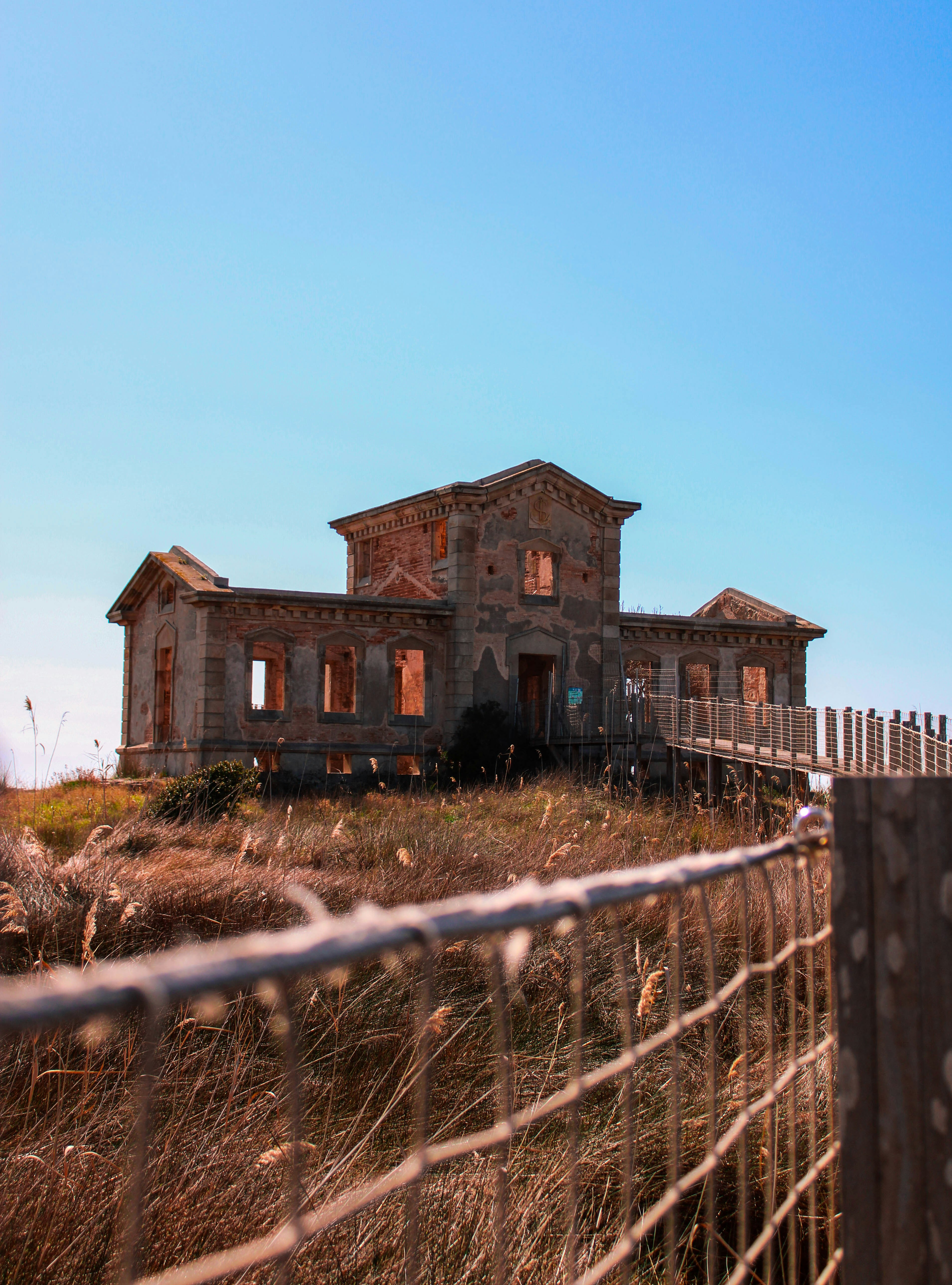 Hilltop Ruin: Weathered Stone House Framed by Wire and Sky
