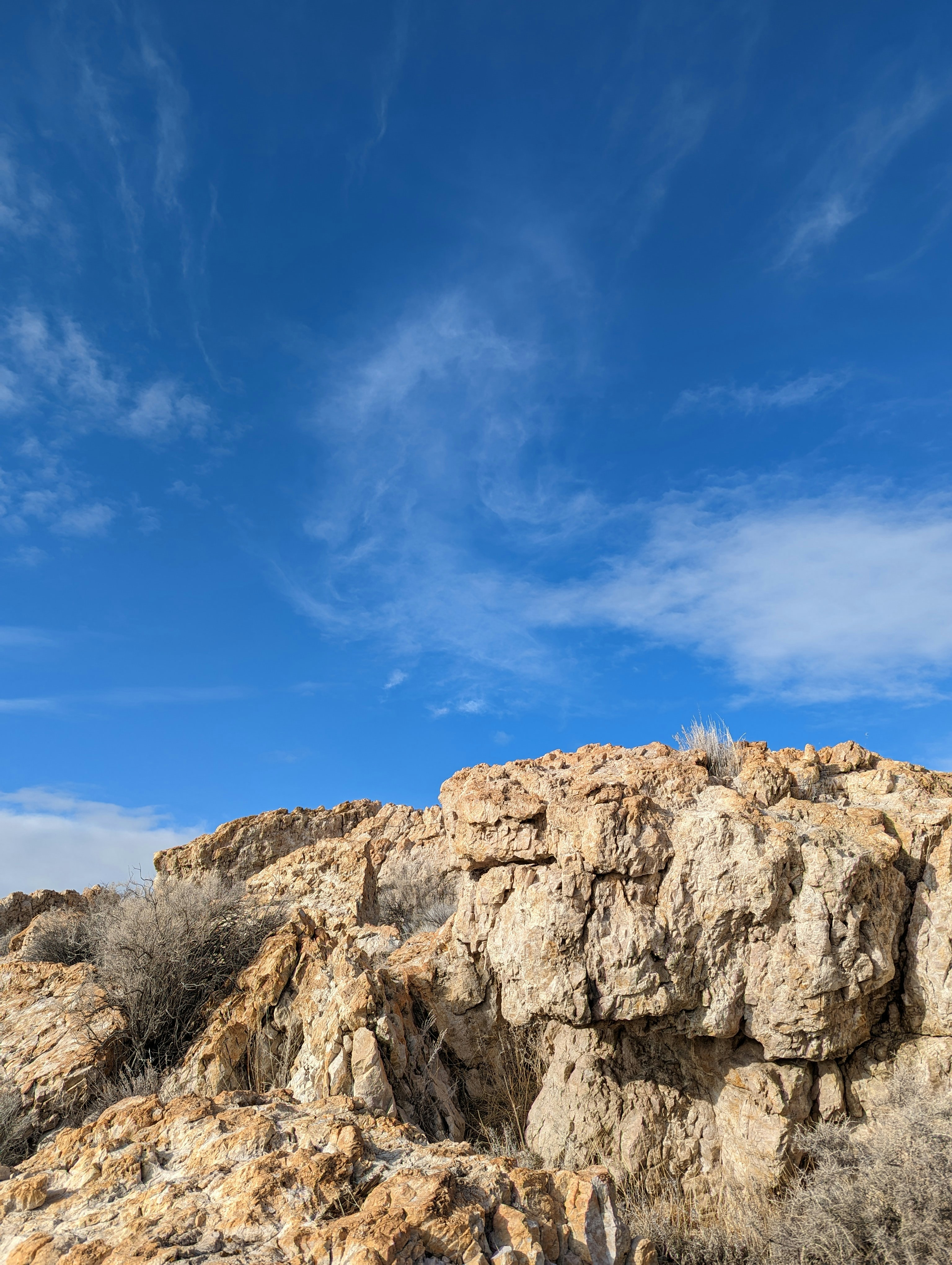 Rugged rock formations under a vast blue sky, punctuated by wispy clouds. The scene captures the stark beauty of a desert landscape.