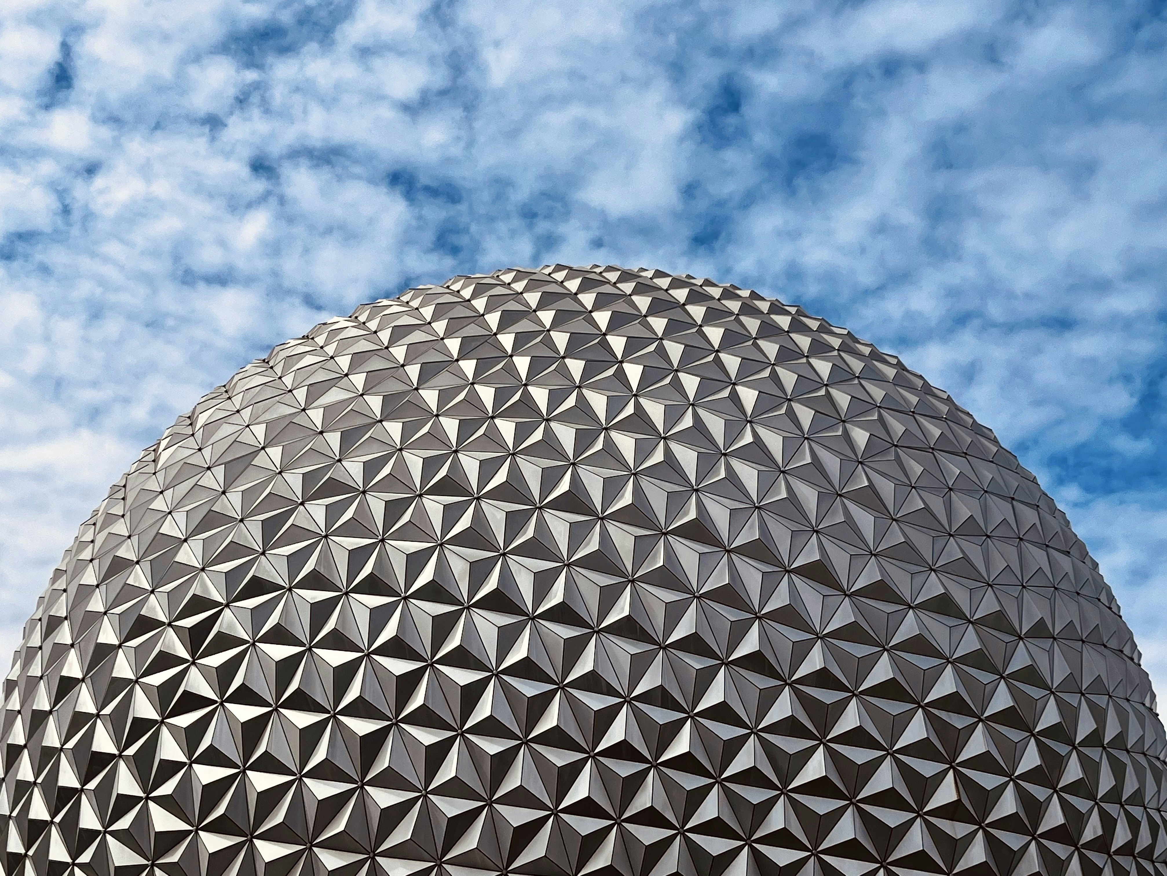 Close-up of a geodesic dome showcasing intricate triangular patterns against a blue sky with scattered clouds.