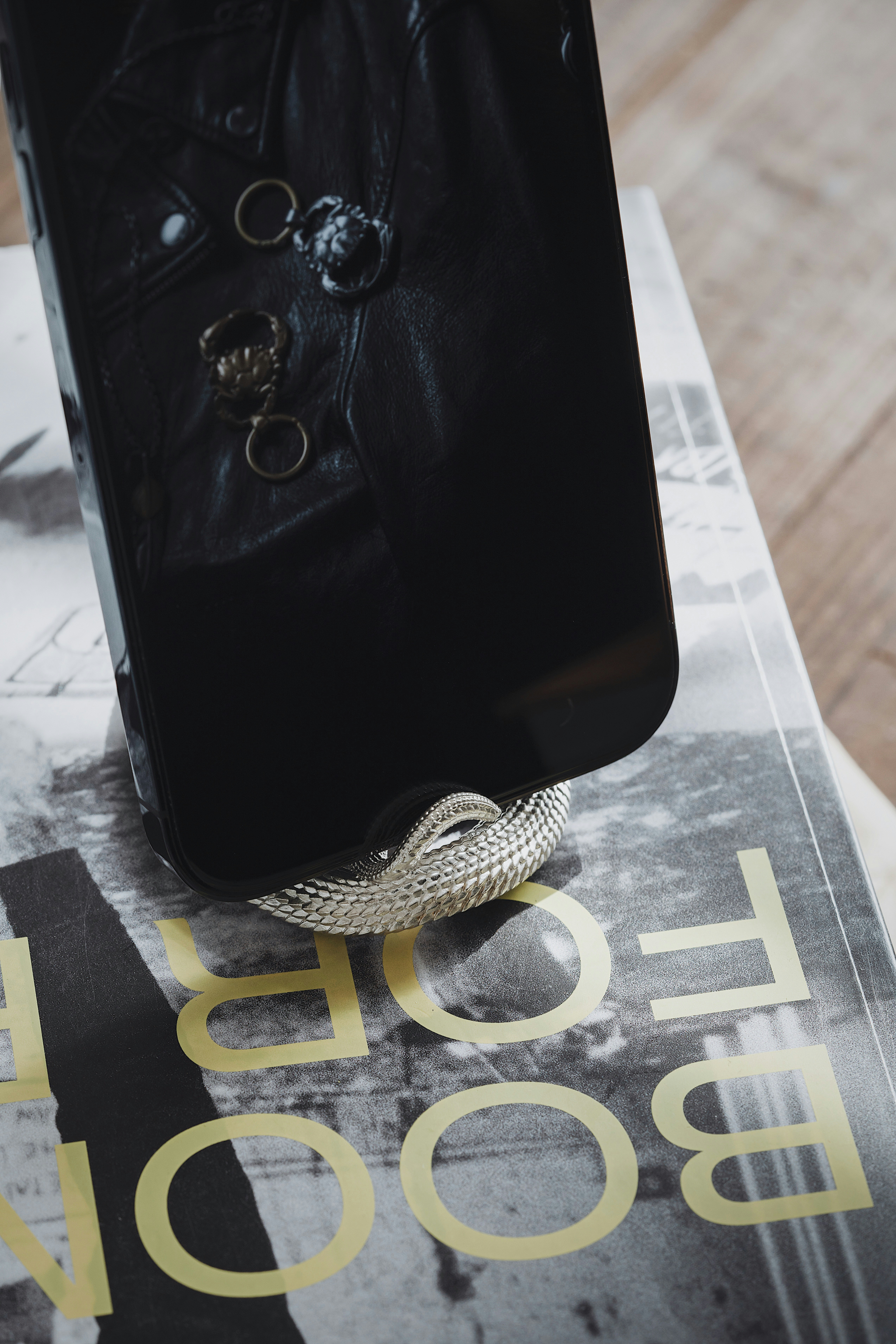 Leather and Coil: a close-up of a smartphone resting on a silver snake ring atop a magazine