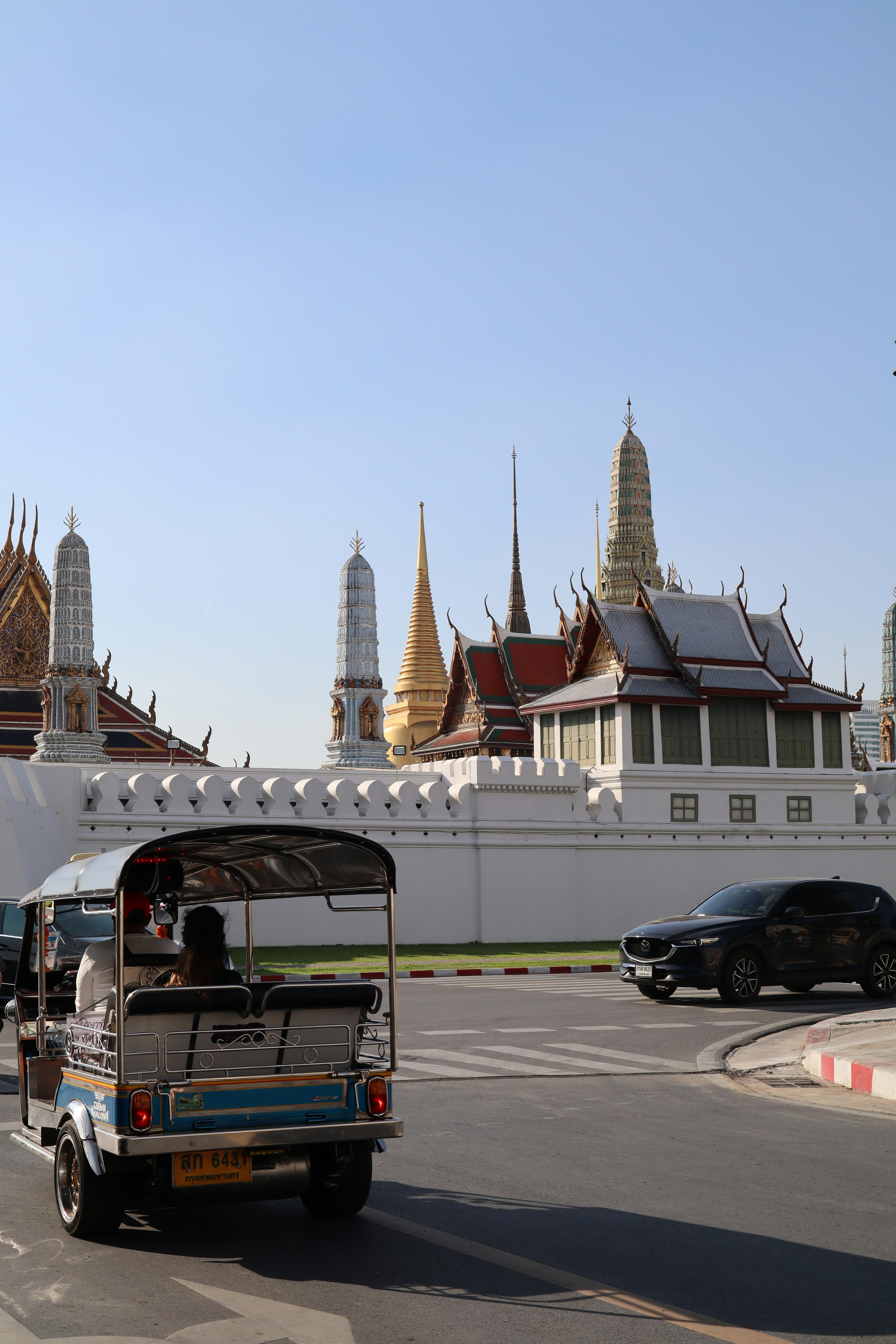 Tuk-tuk navigating a street lined with ornate temples and spires under a clear blue sky.