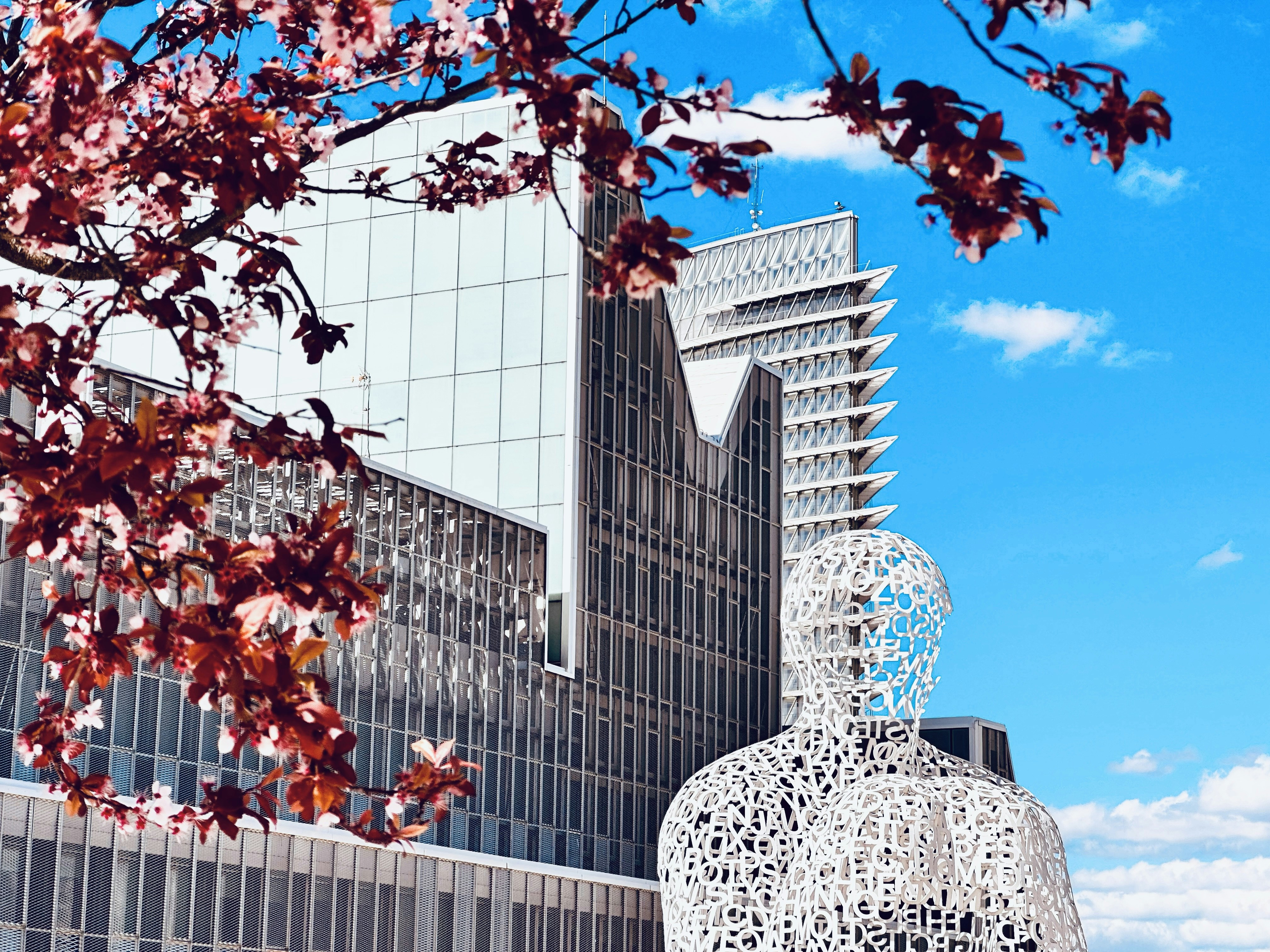 A striking white sculpture stands against a backdrop of modern architecture and vibrant foliage, embodying the fusion of art and design.