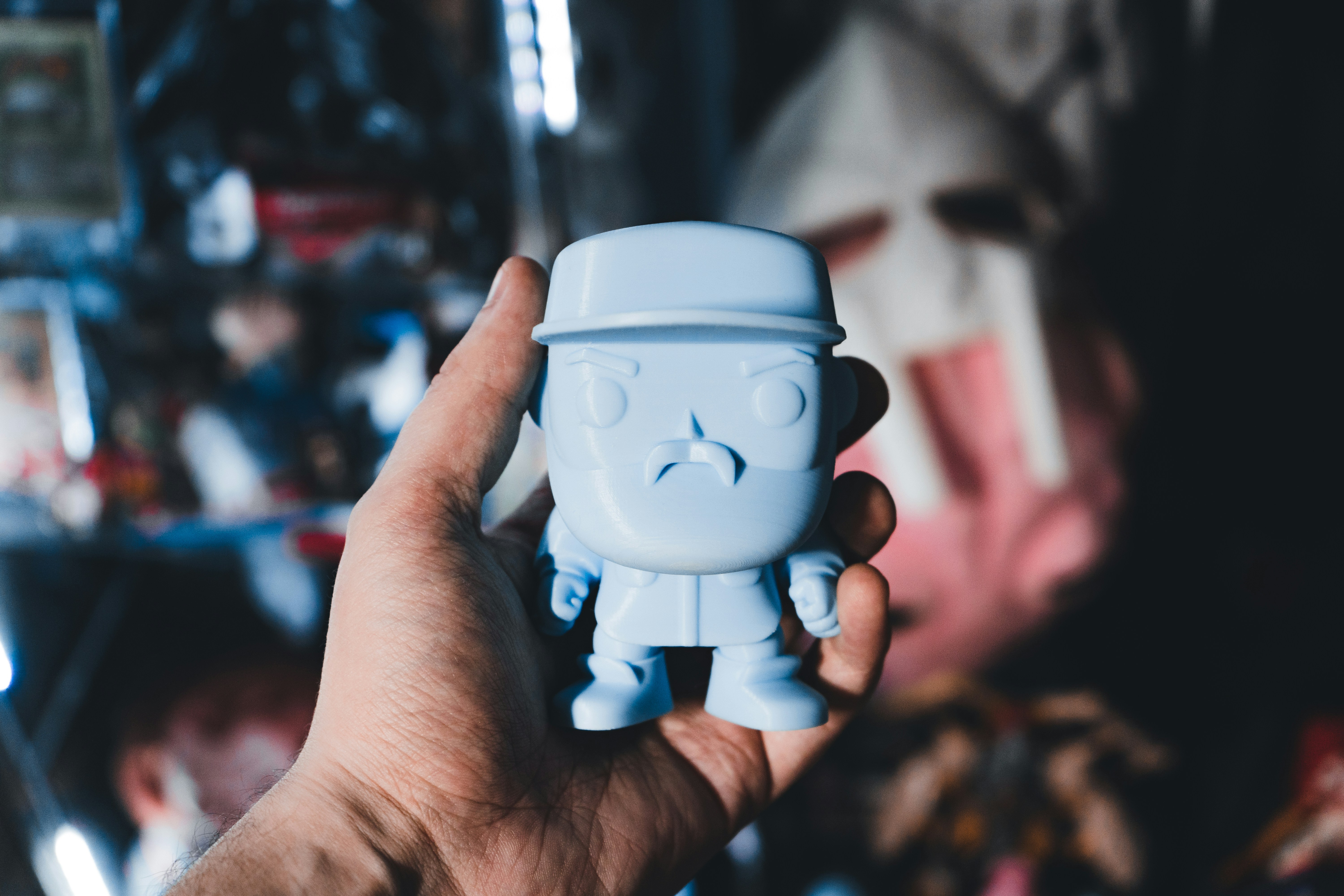 Blue vinyl figurine gripped in a hand amid neon-lit clutter