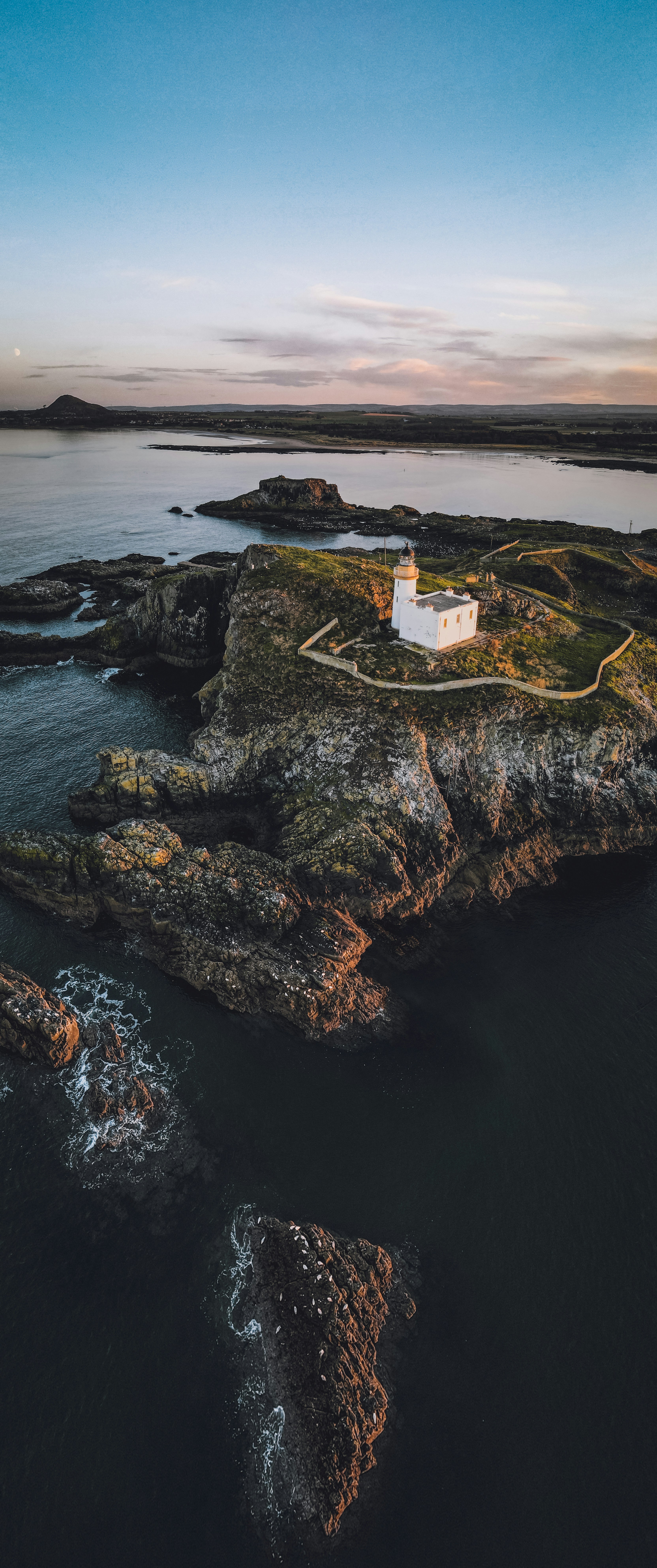 A lighthouse perched on rugged cliffs, surrounded by the tranquil sea at dusk, highlighting the harmony between nature and human craftsmanship.