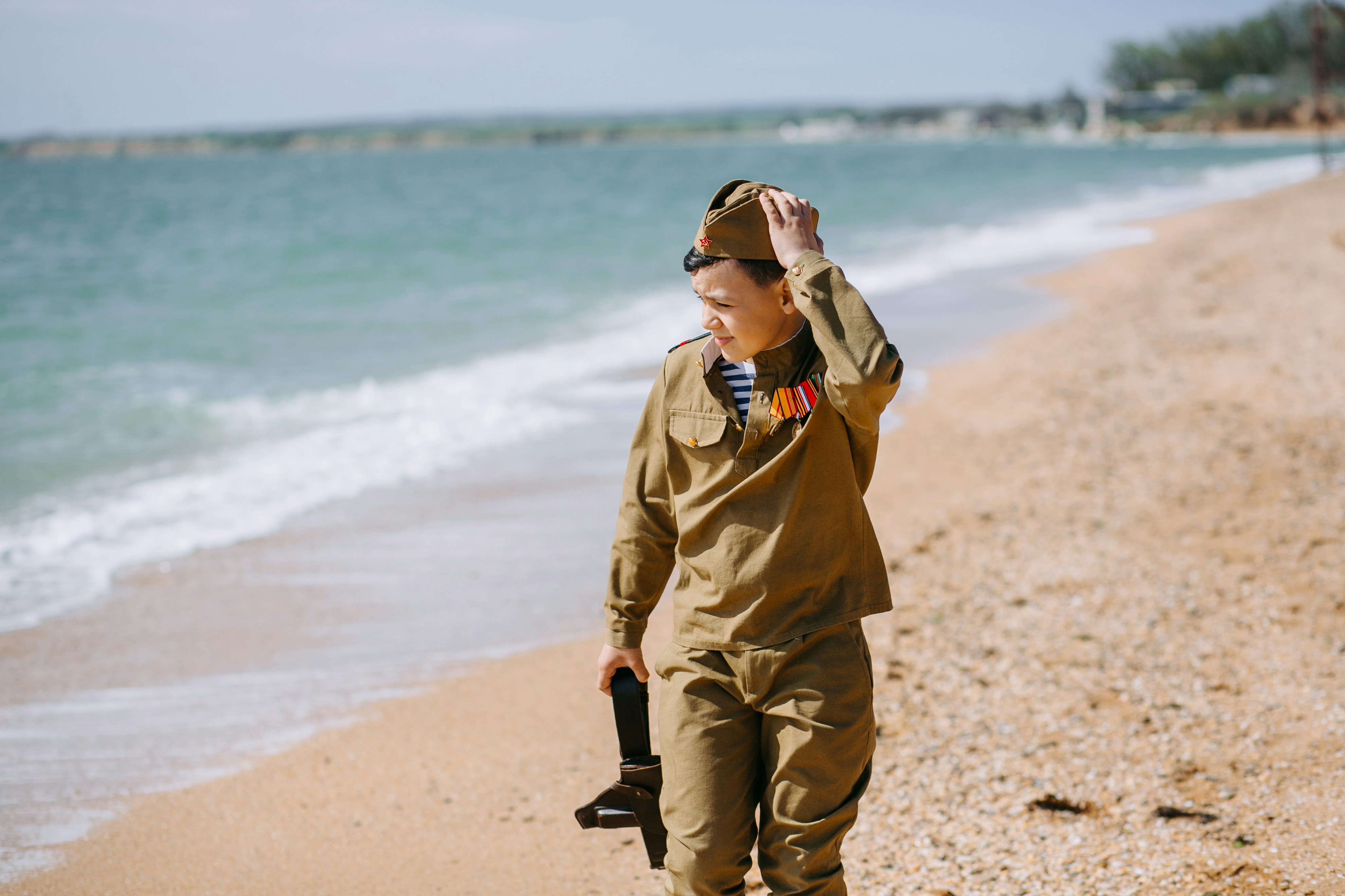 Explorer on a Sandy Shore: A Child in Tan Uniform with a Toy Gun by the Sea