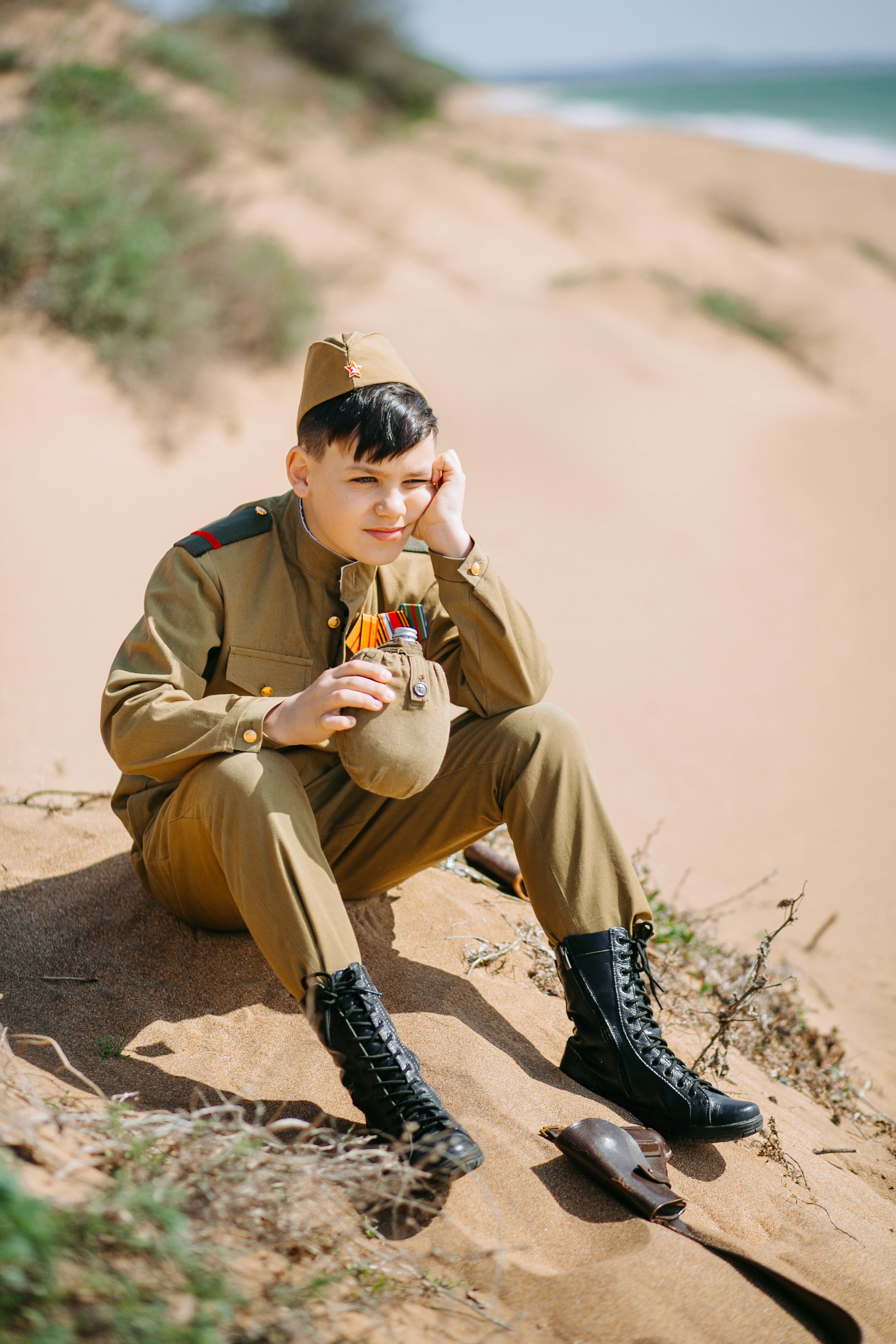 A boy in a military uniform sitting on a beach photo – Free Boy Image ...