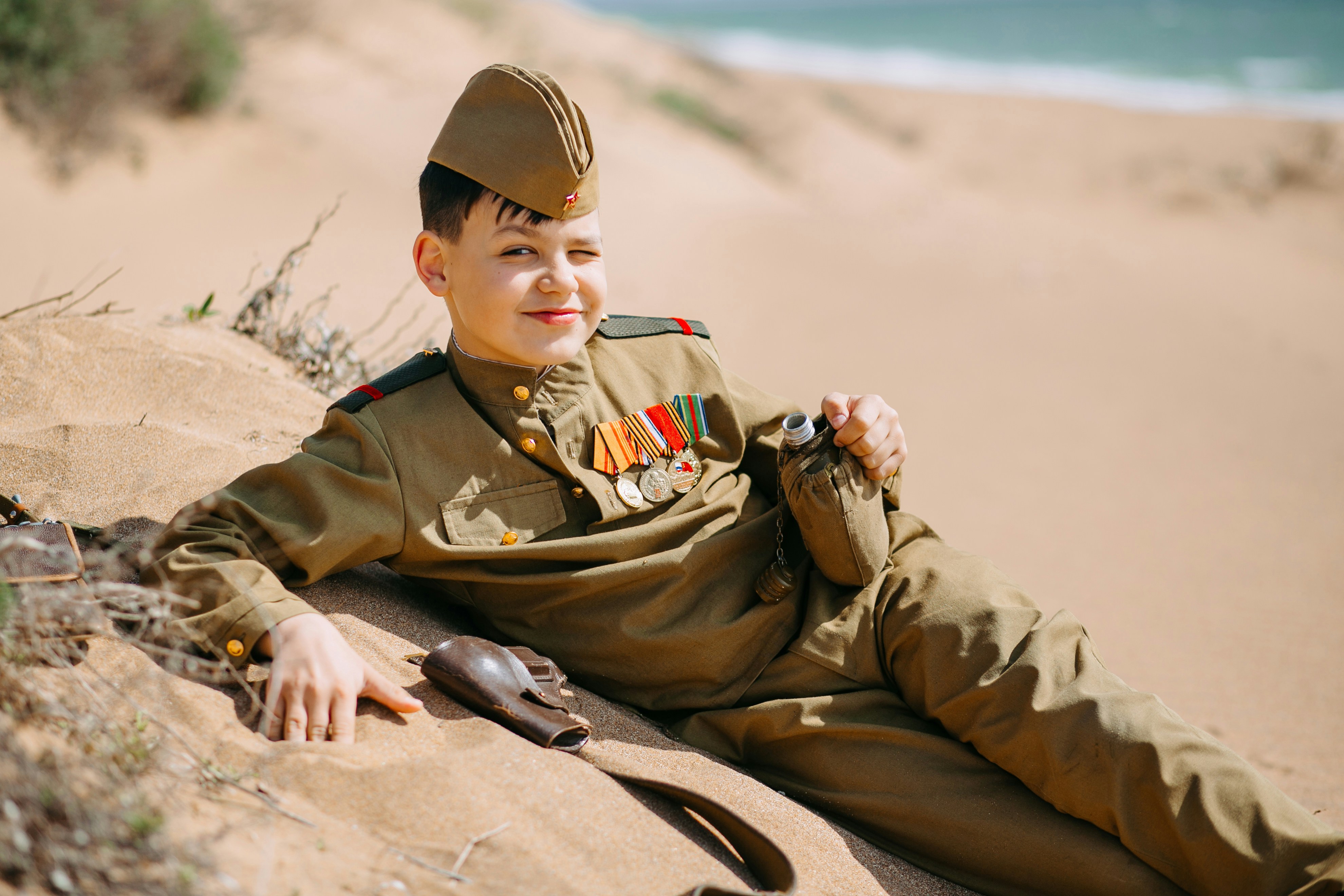 A boy in a military uniform laying on the sand photo – Free Boy Image ...