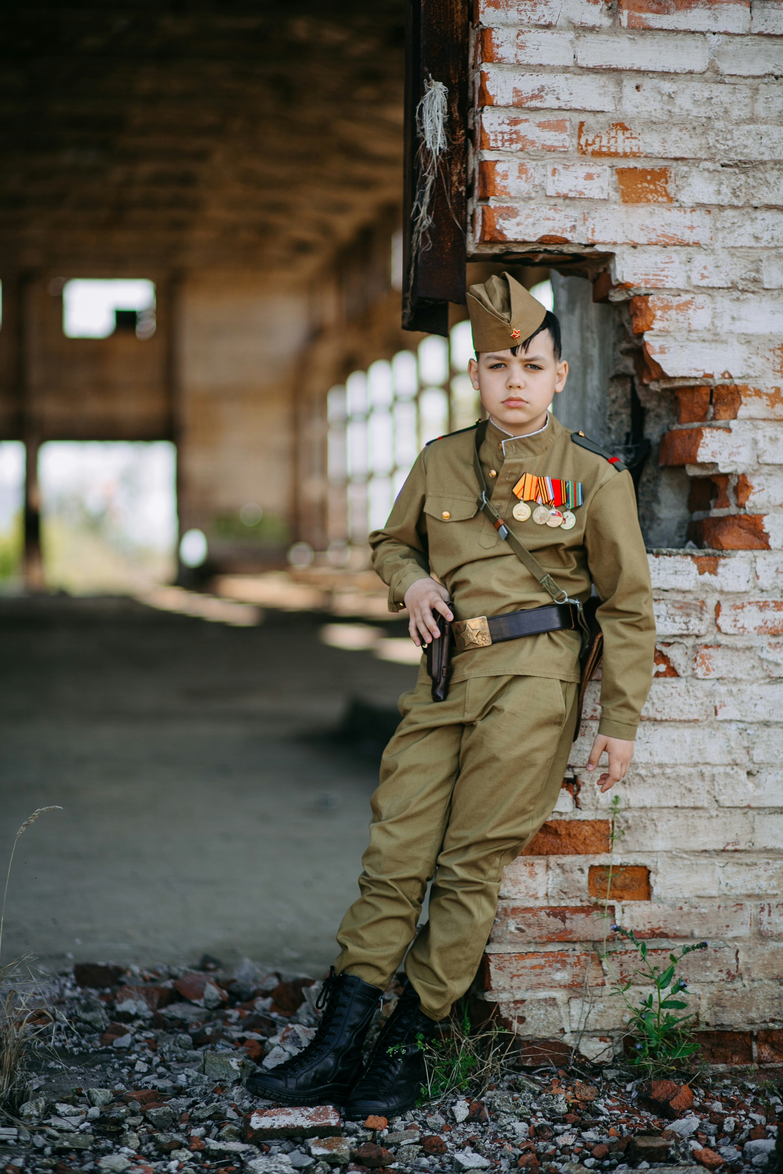 A young boy in a military uniform leaning against a brick wall photo ...
