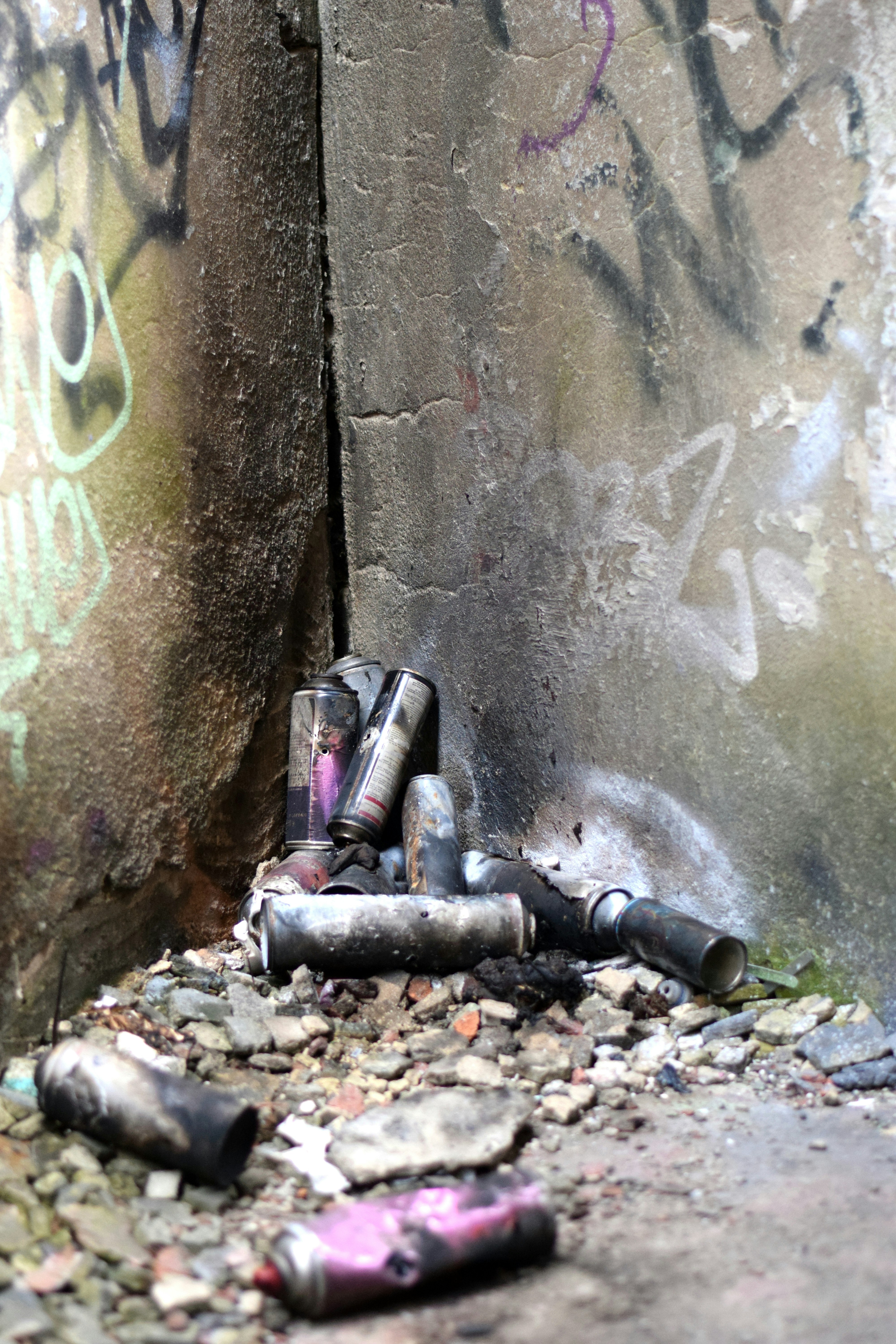 Abandoned spray paint cans scattered among rubble in a graffiti-laden alleyway.