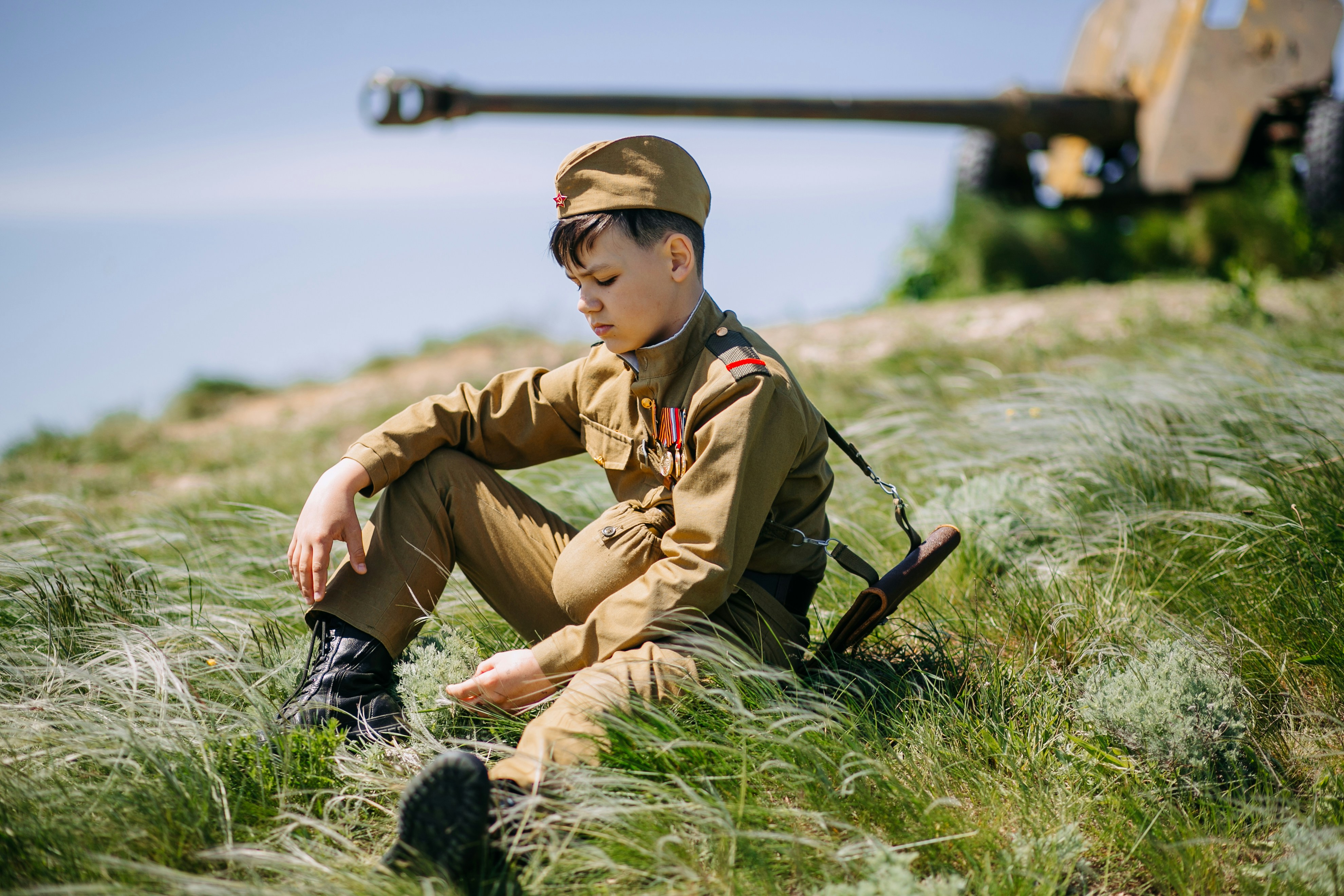 Quiet Pause in Uniform: Grassland Portrait with a Tank in the Background