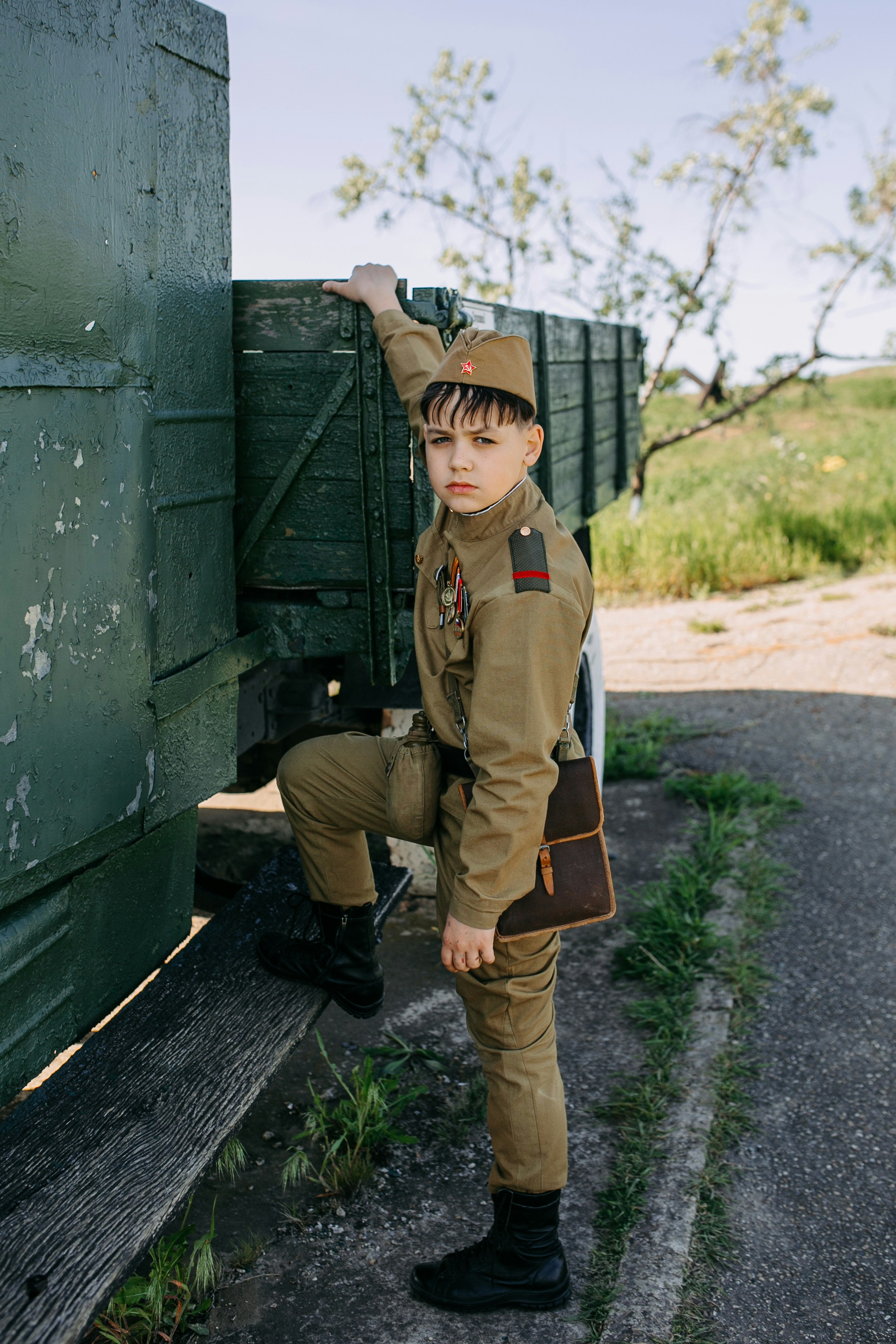 a young boy dressed in a military uniform leaning against a truck