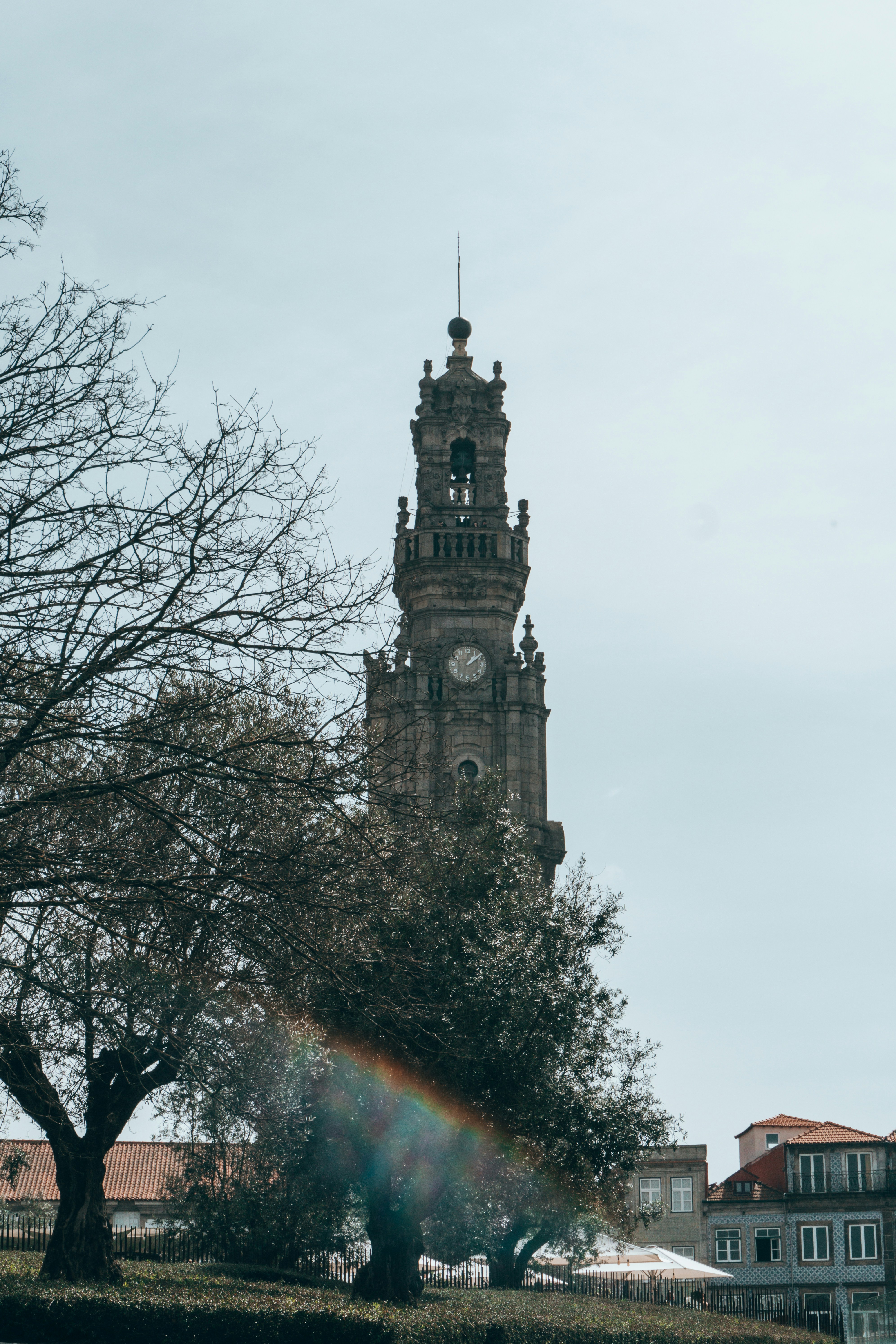 The Timekeeper Beneath a Pale Sky: Clocktower, Bare Trees, and a Faint Rainbow