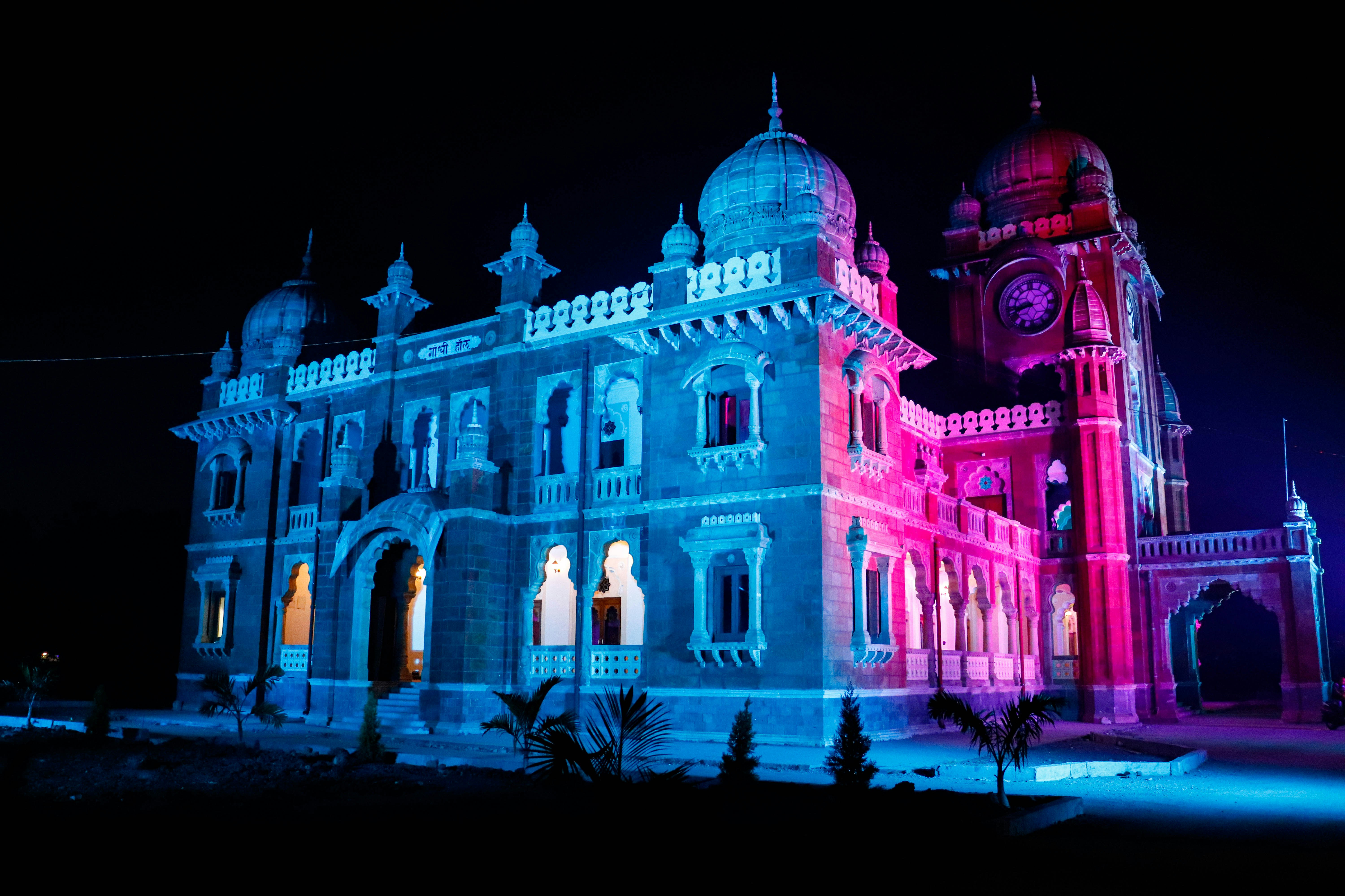 Historic building illuminated with vibrant blue and pink lights against a night sky.