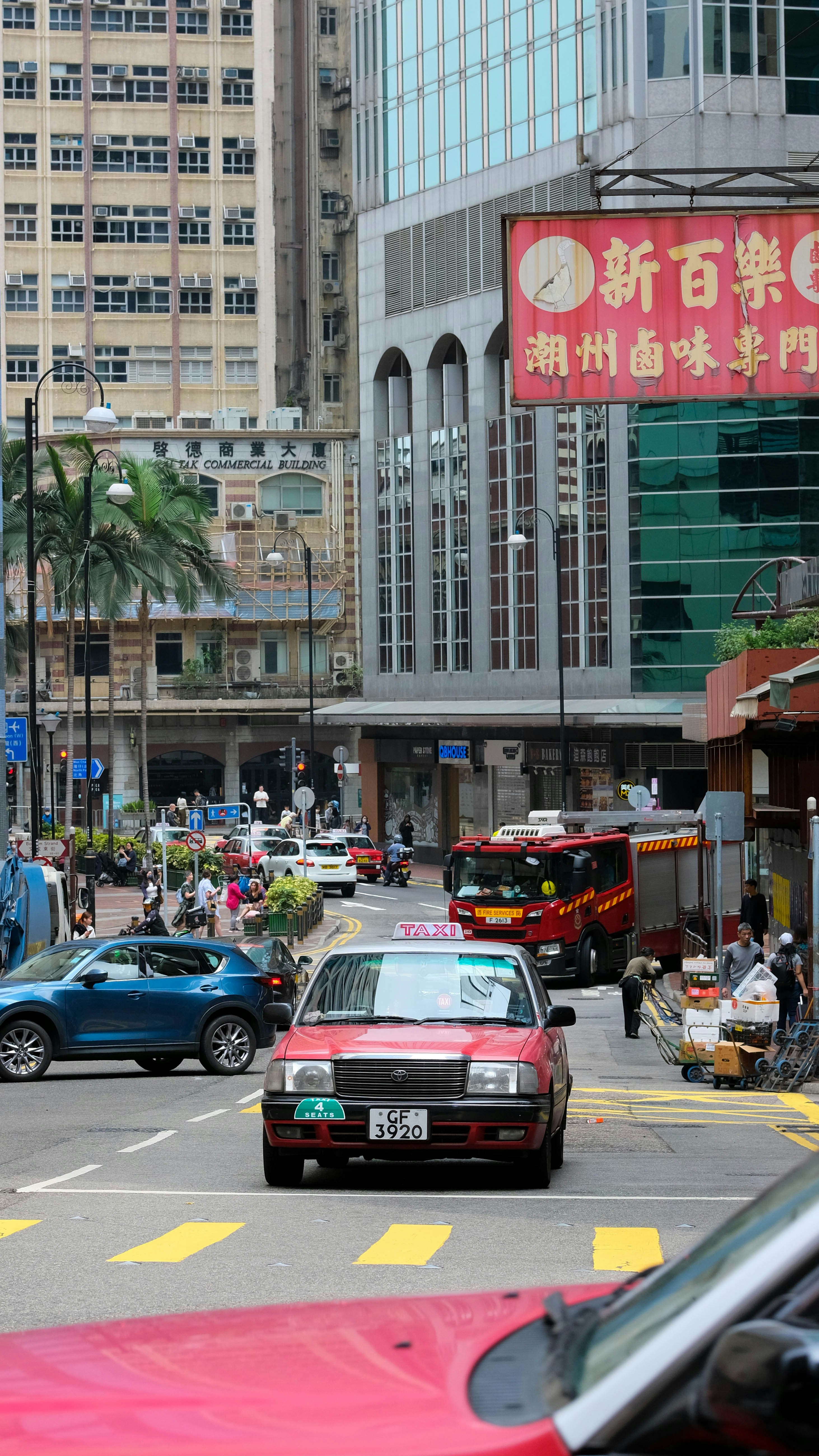 Busy street scene featuring a red taxi navigating through traffic amidst towering buildings and vibrant signage.