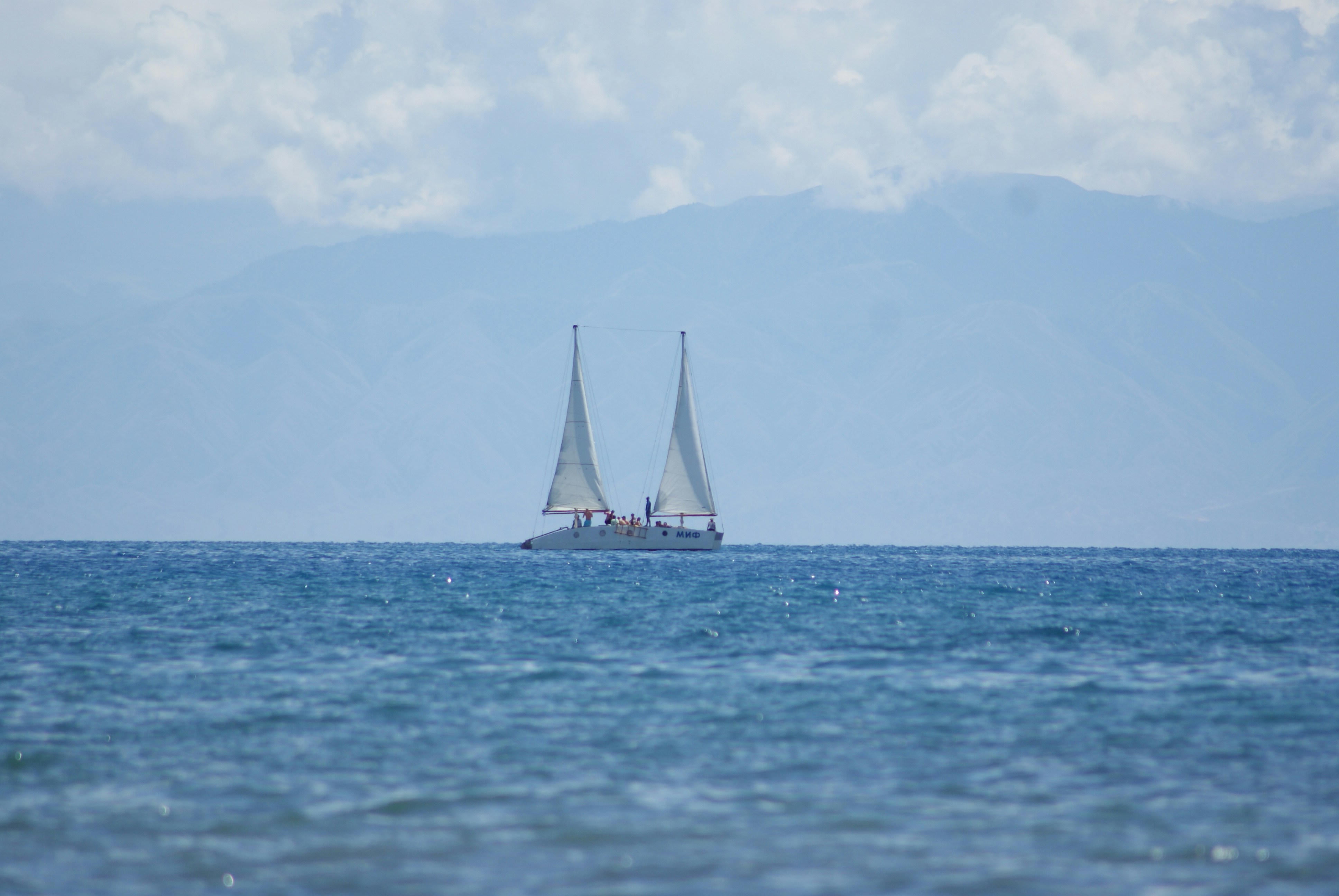 Two-Masted Sailboat on a Quiet Blue Expanse Beneath a Veiled Mountain Range