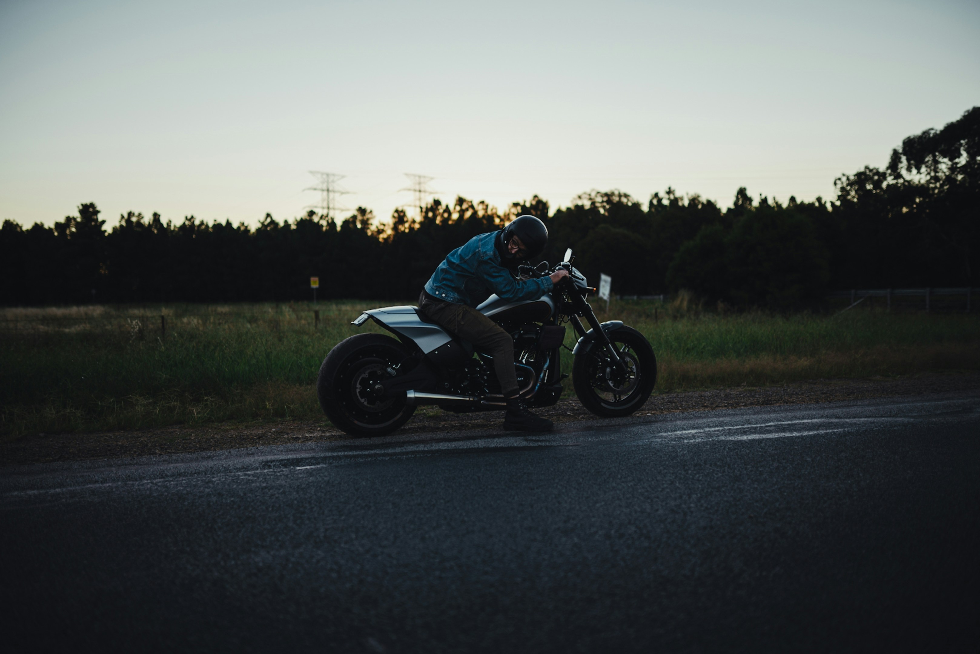 A motorcycle and rider on a dim highway at dusk, bathed in fading light. This is a low-light street photograph.