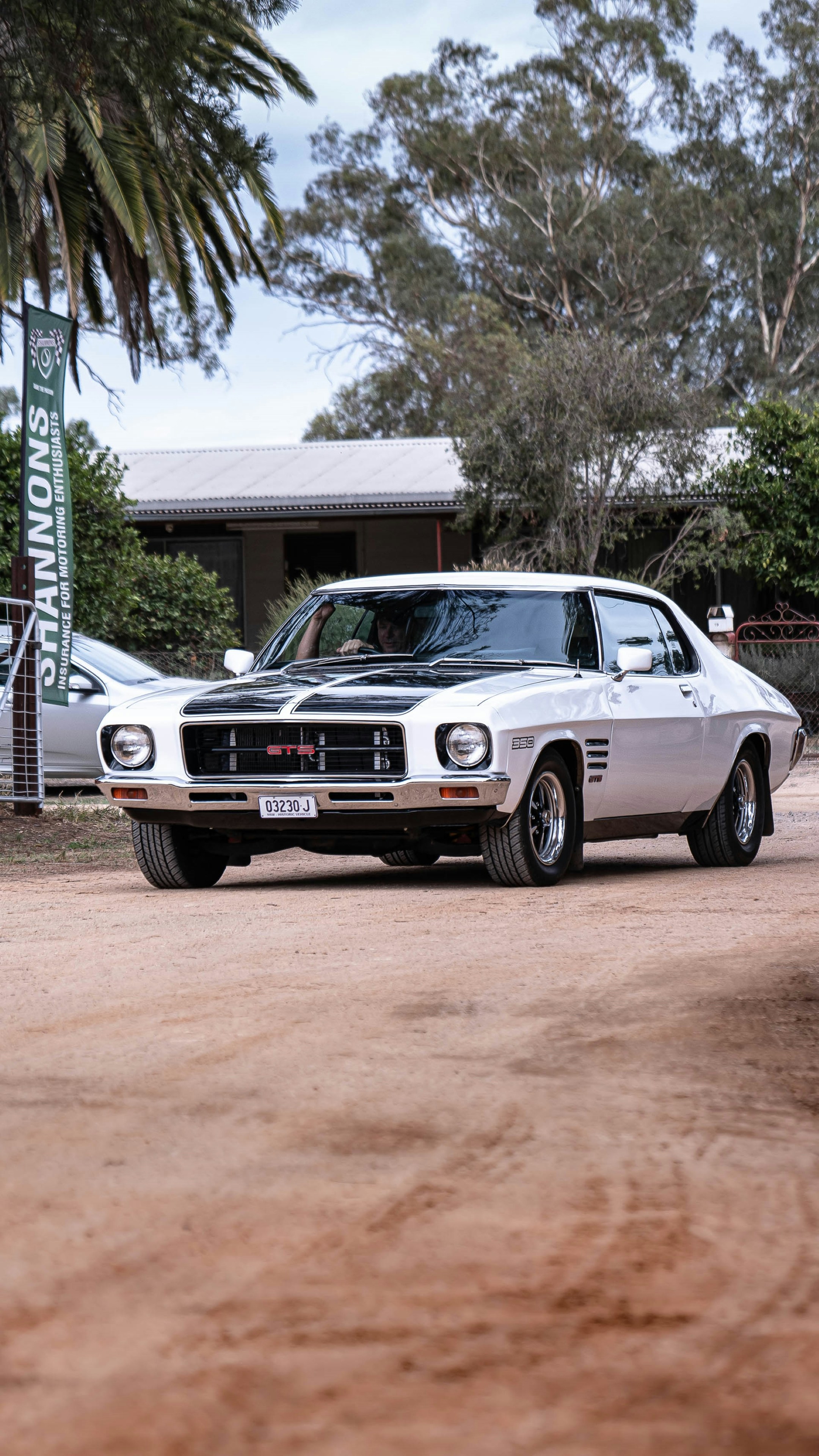Brisk reef-white Classic: a vintage GTL muscle car hugs a dusty driveway