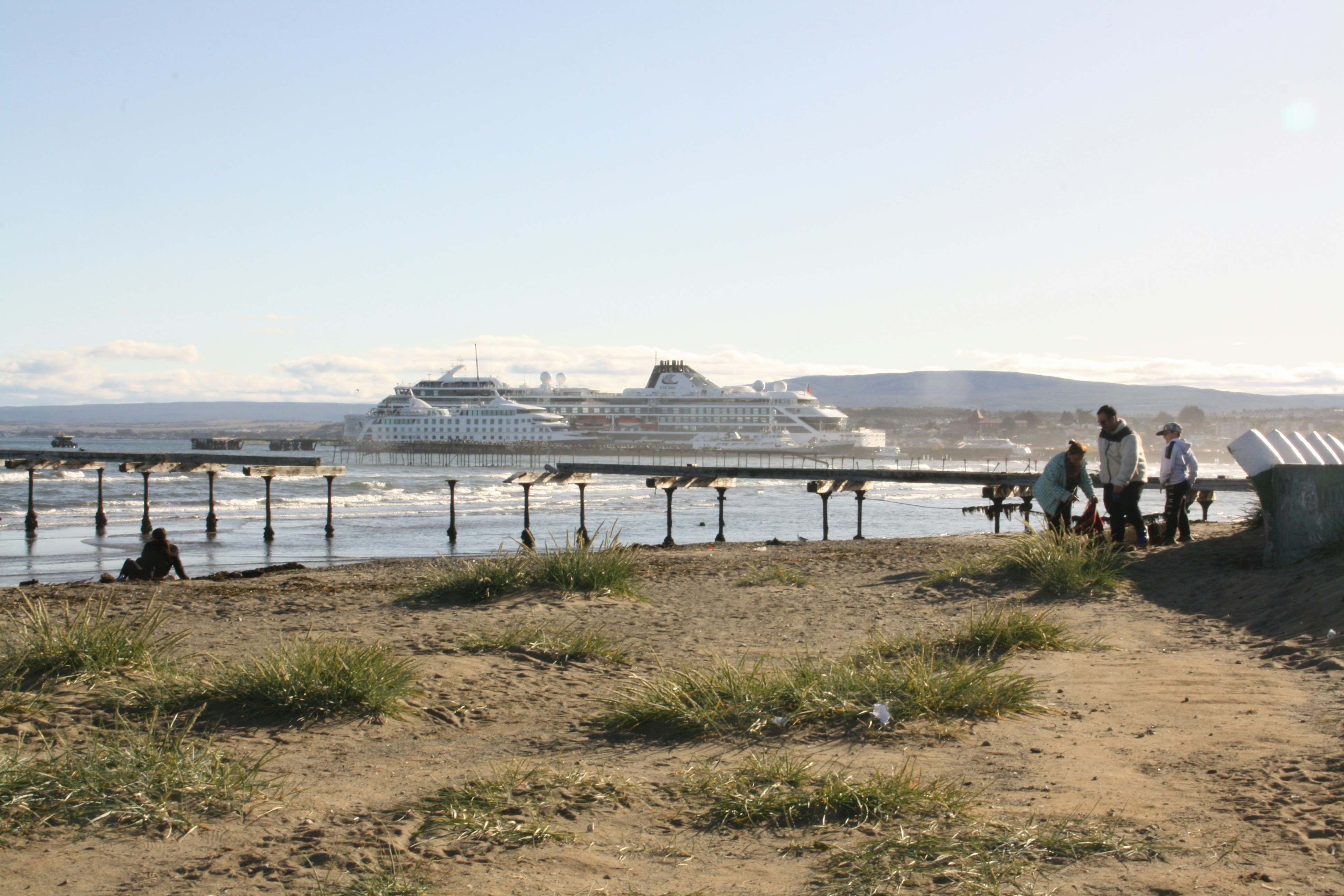 People enjoying leisure time on a sandy beach with a distant cruise ship anchored in calm waters.