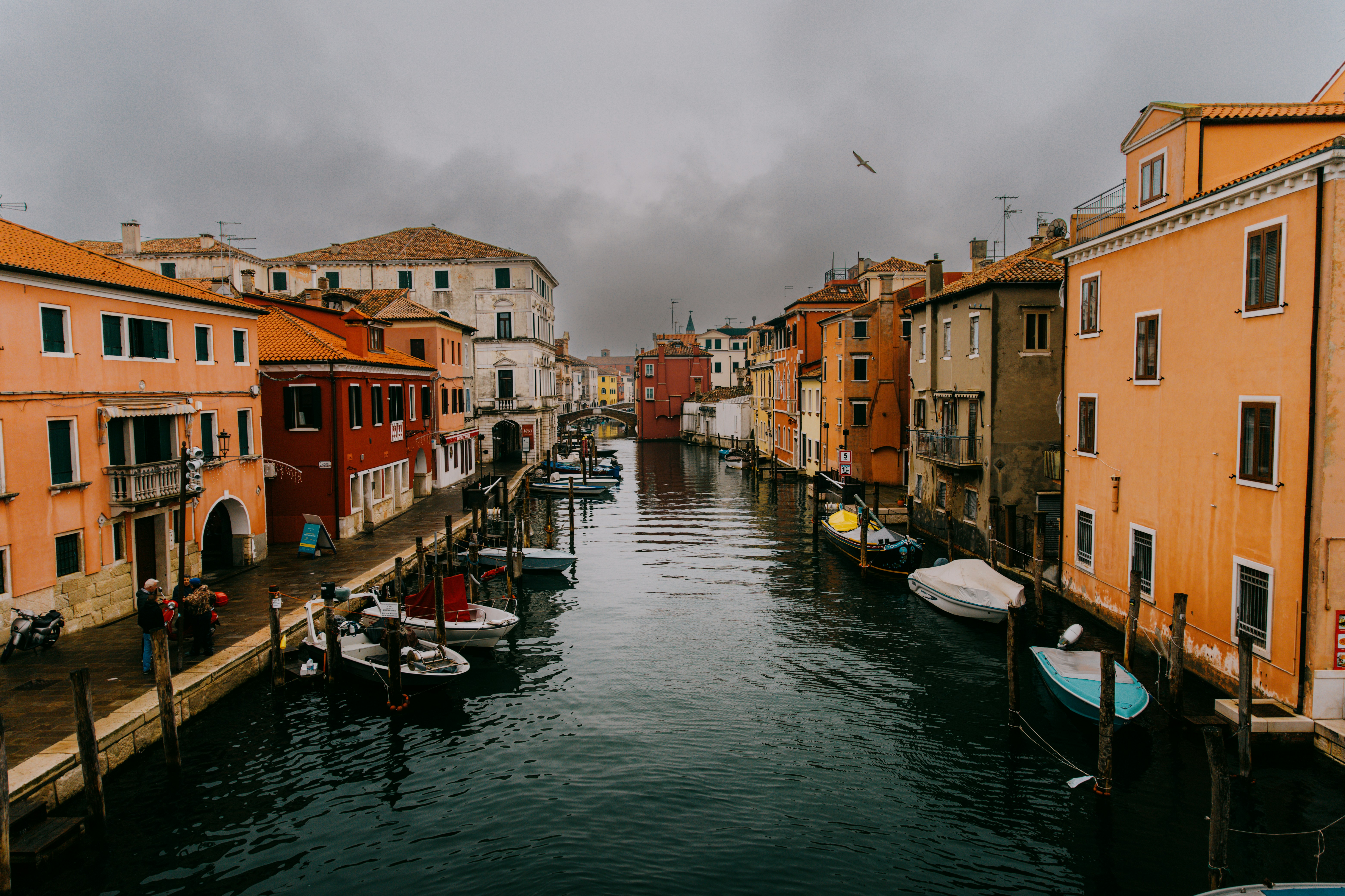 Narrow waterway lined with colorful buildings and moored boats under a cloudy sky.