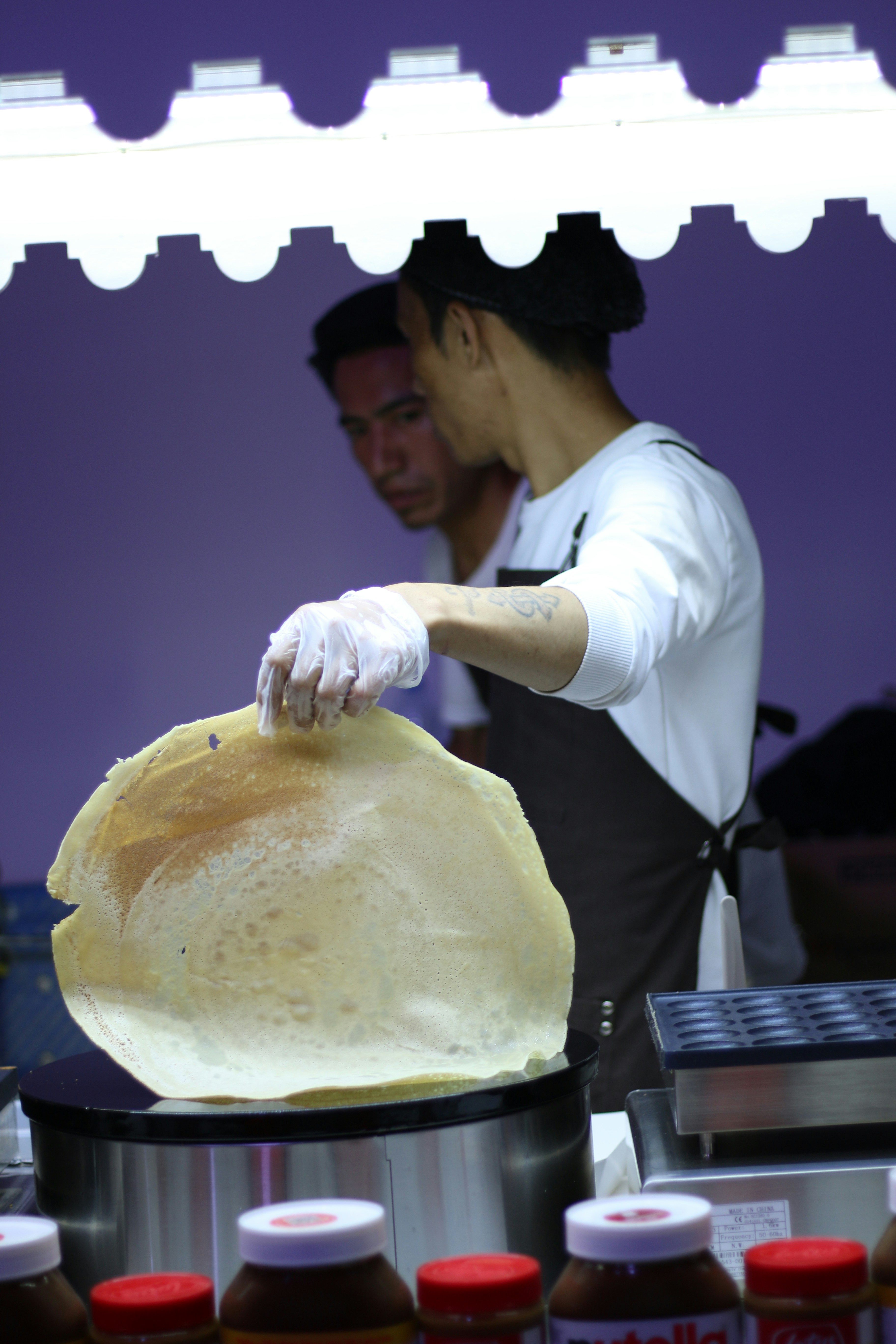Purple-lit Crepe Station: Hands, Heat, and a Perfect Flip