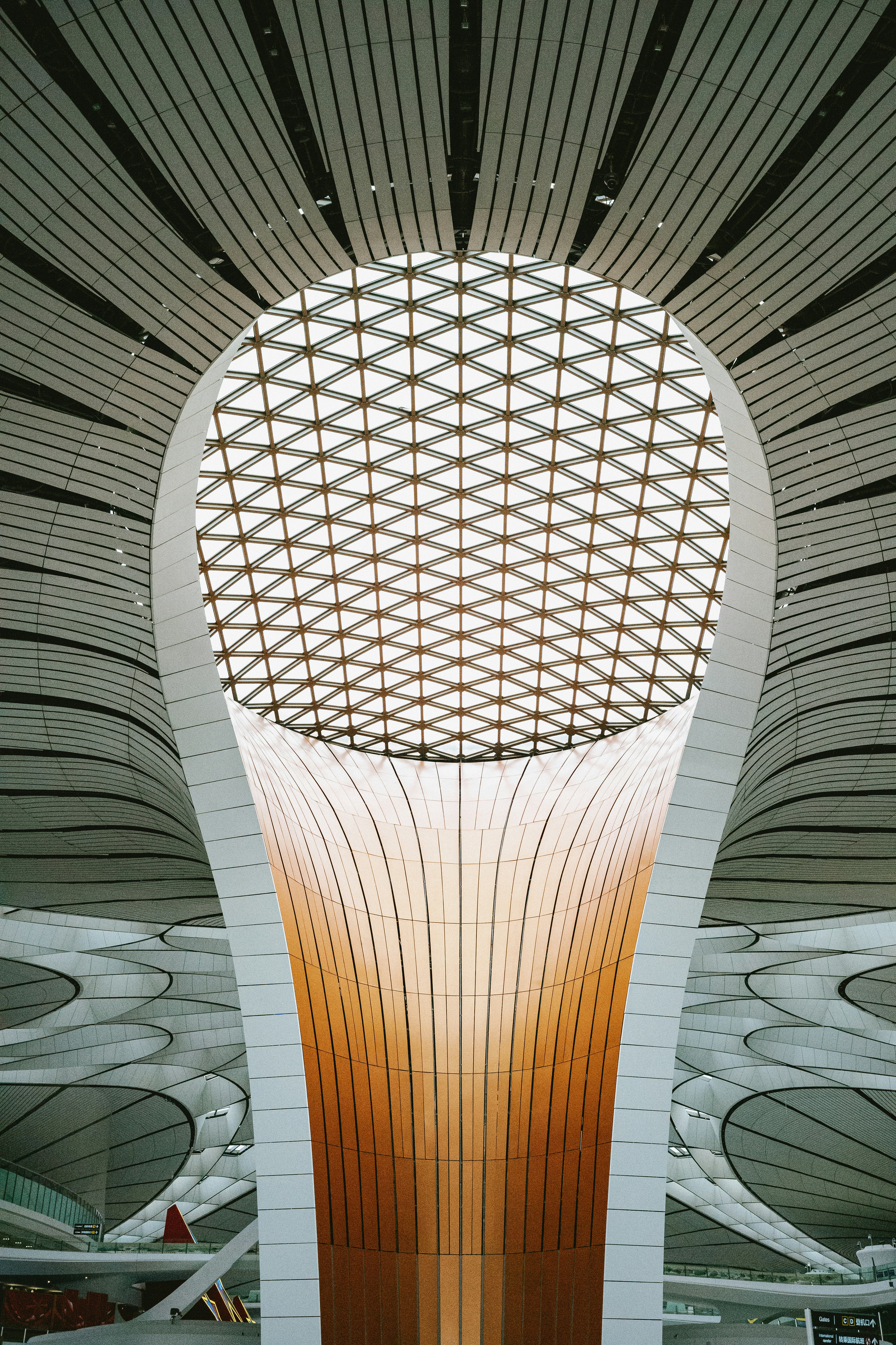 Interior of a modern transit hall featuring a circular lattice skylight framed by sweeping curved arches, bathed in warm amber light.