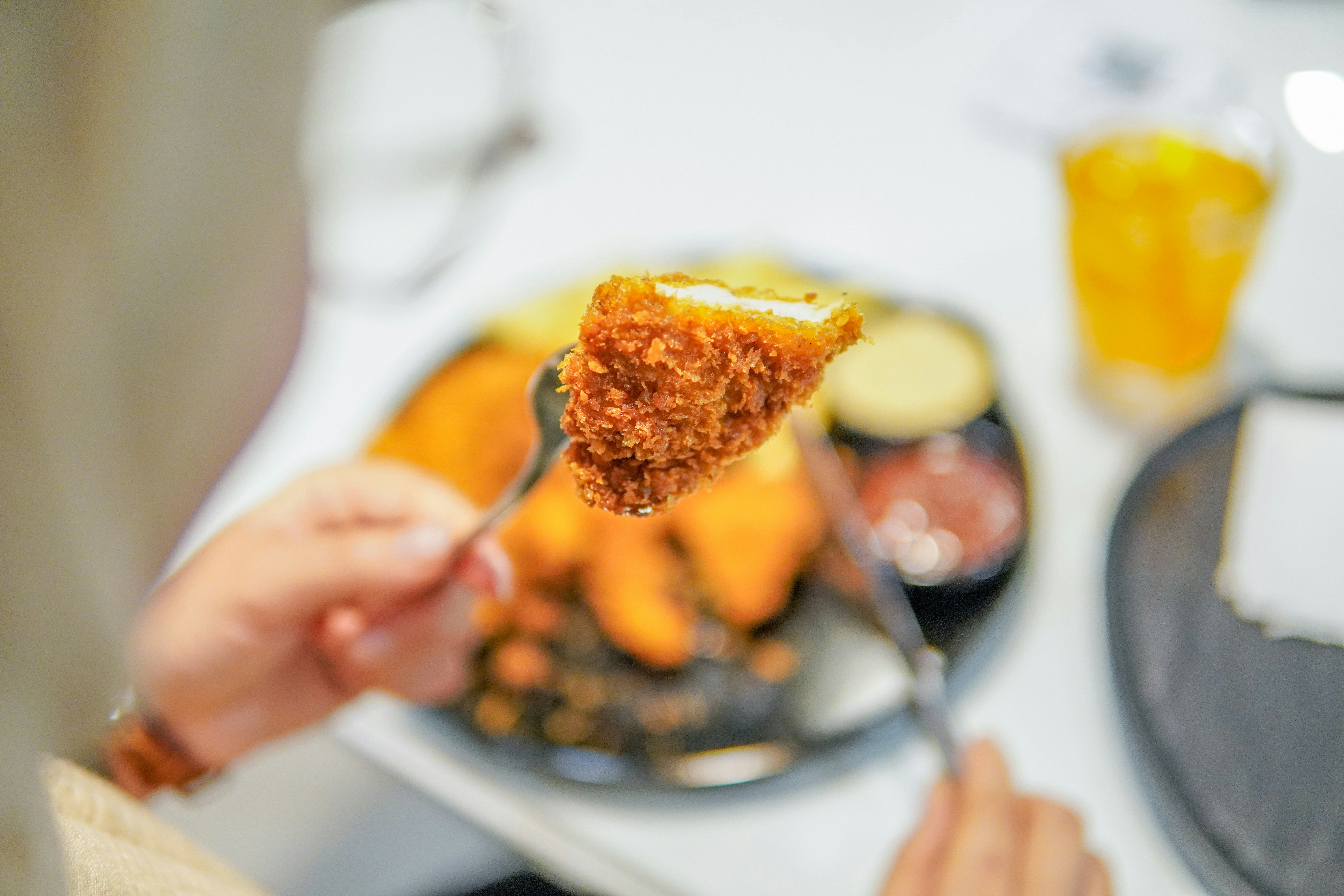 Close-up of a fork holding a piece of breaded food above a plate with various accompaniments.