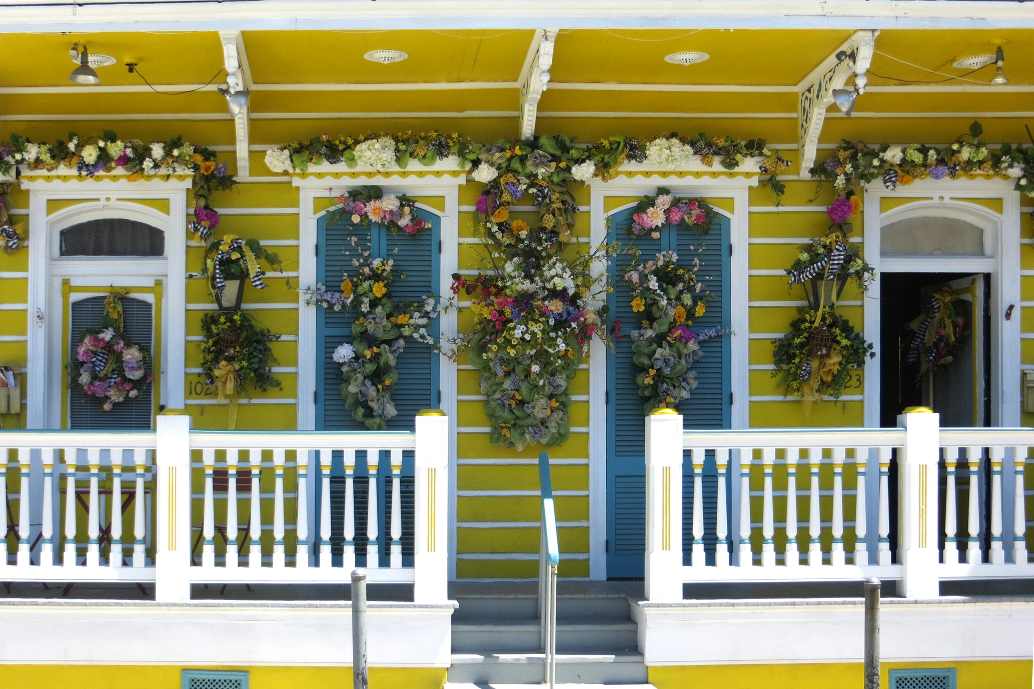 Bright yellow house adorned with colorful floral wreaths and blue shutters, showcasing a lively exterior decor. The inviting porch adds to the cheerful ambiance.