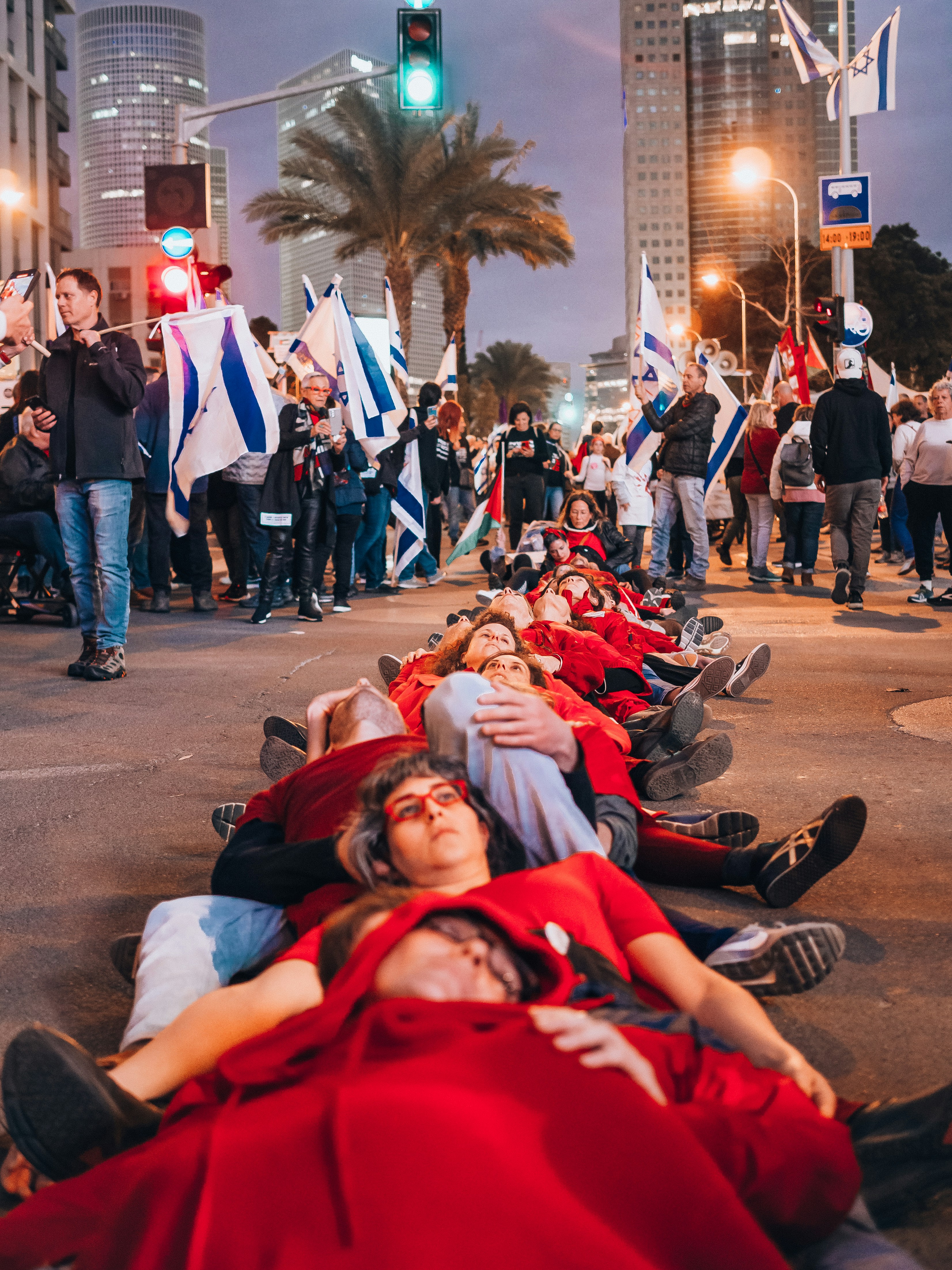 Red-Robed Protesters Lined Across a City Street as Flags Rise at Dusk