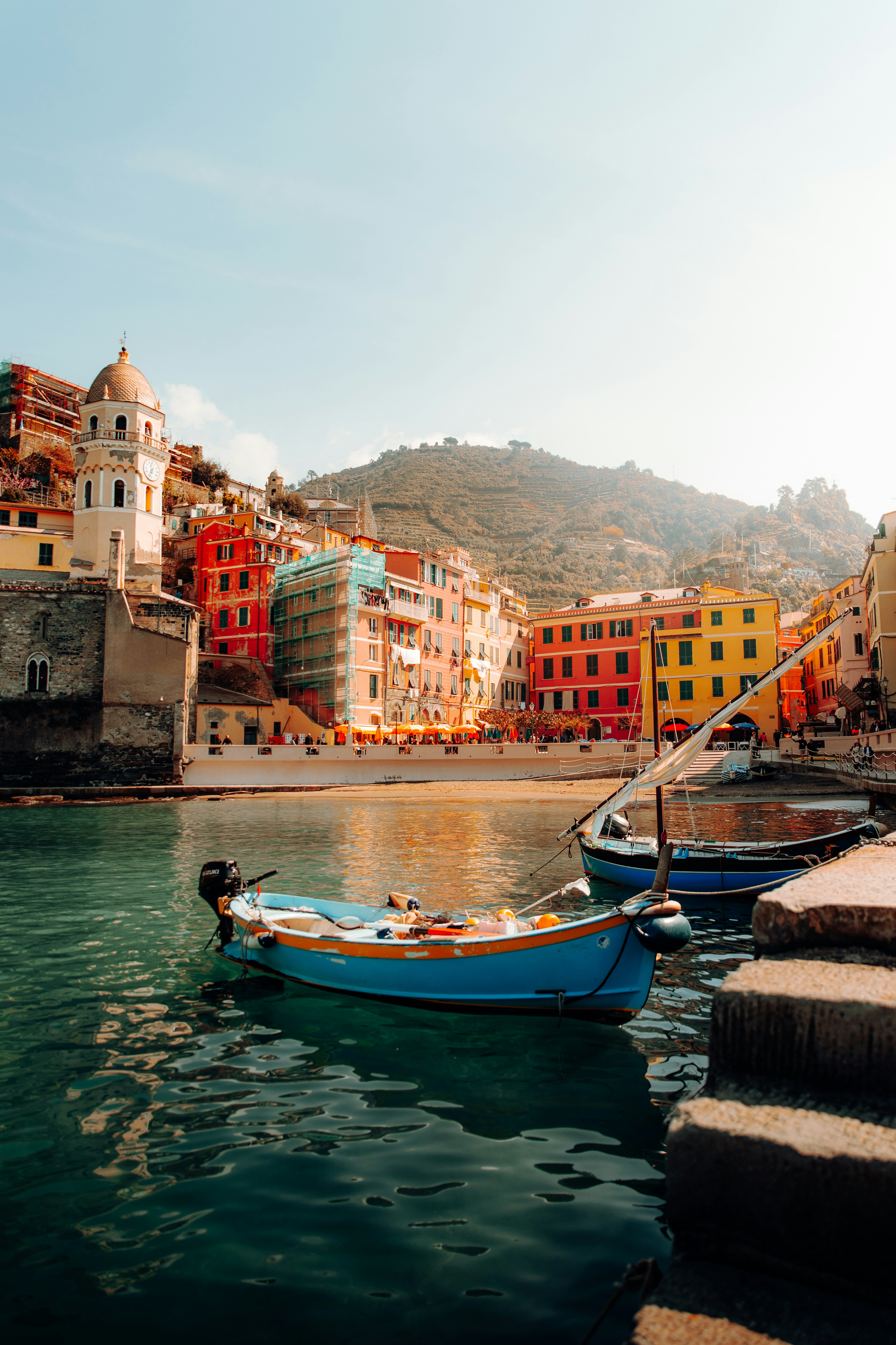 Colorful boats anchored in a tranquil harbor, surrounded by vibrant buildings and lush hills. The scene captures the essence of coastal life.