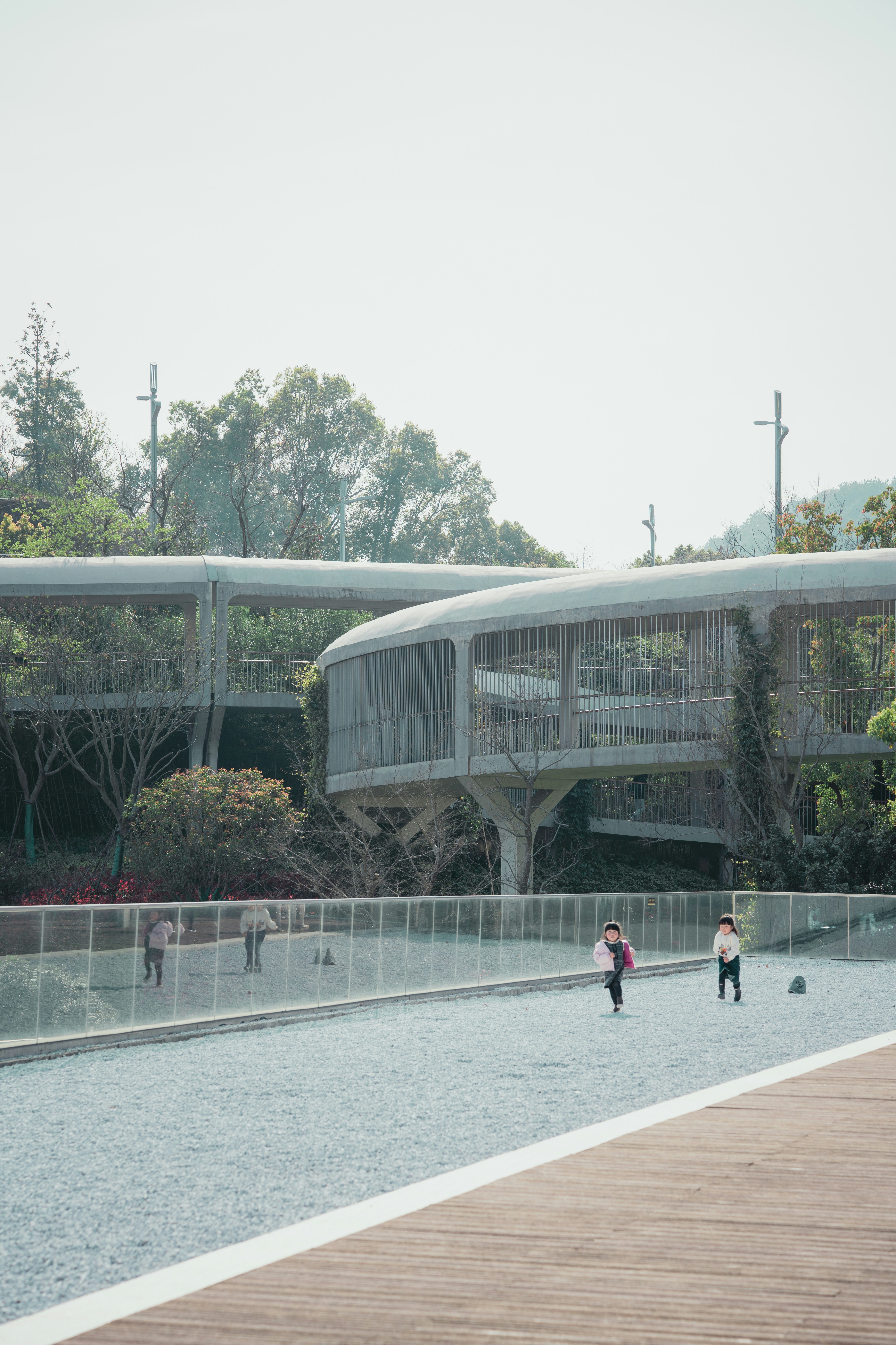 Under the Curve: Two Pedestrians on a Riverside Boardwalk Beneath a Modern Overpass