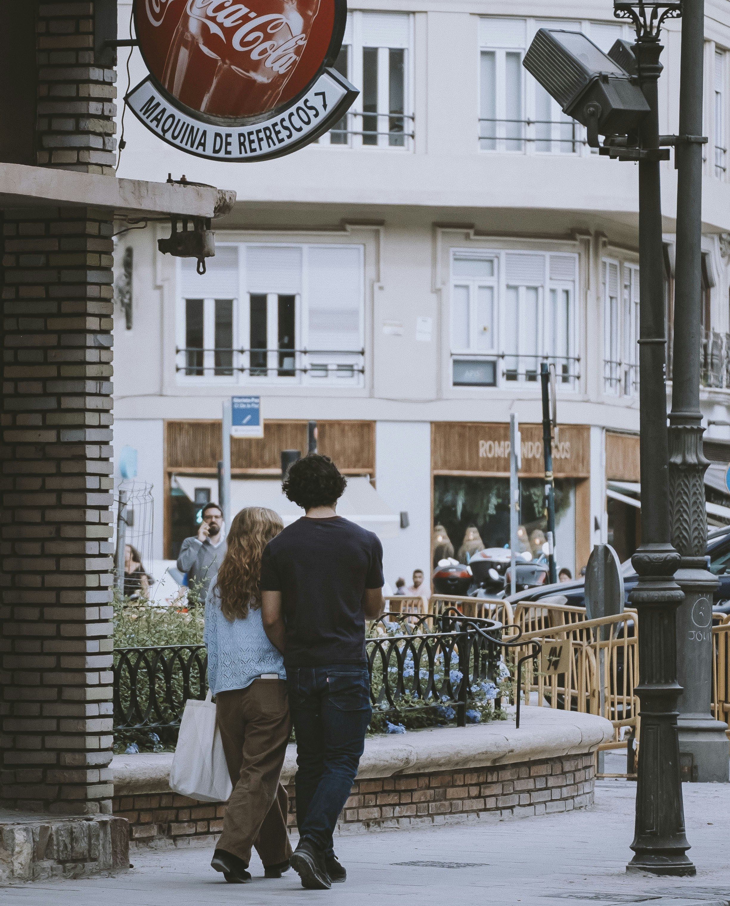Couple walking hand-in-hand past a vintage Coca-Cola sign in a bustling city street, capturing a blend of nostalgia and modern life.