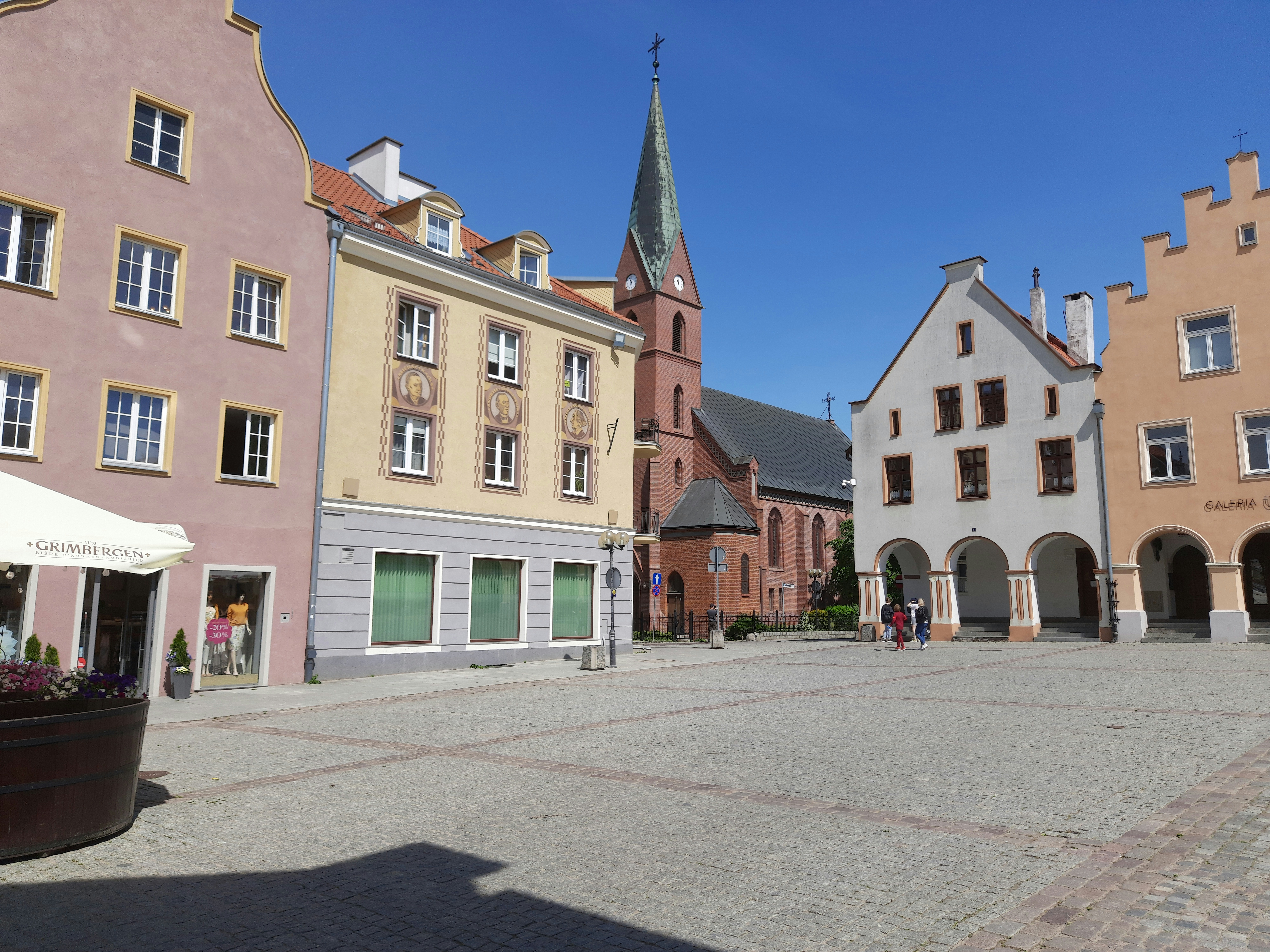 Colorful historic buildings surround a quiet, sunlit square under a clear blue sky.