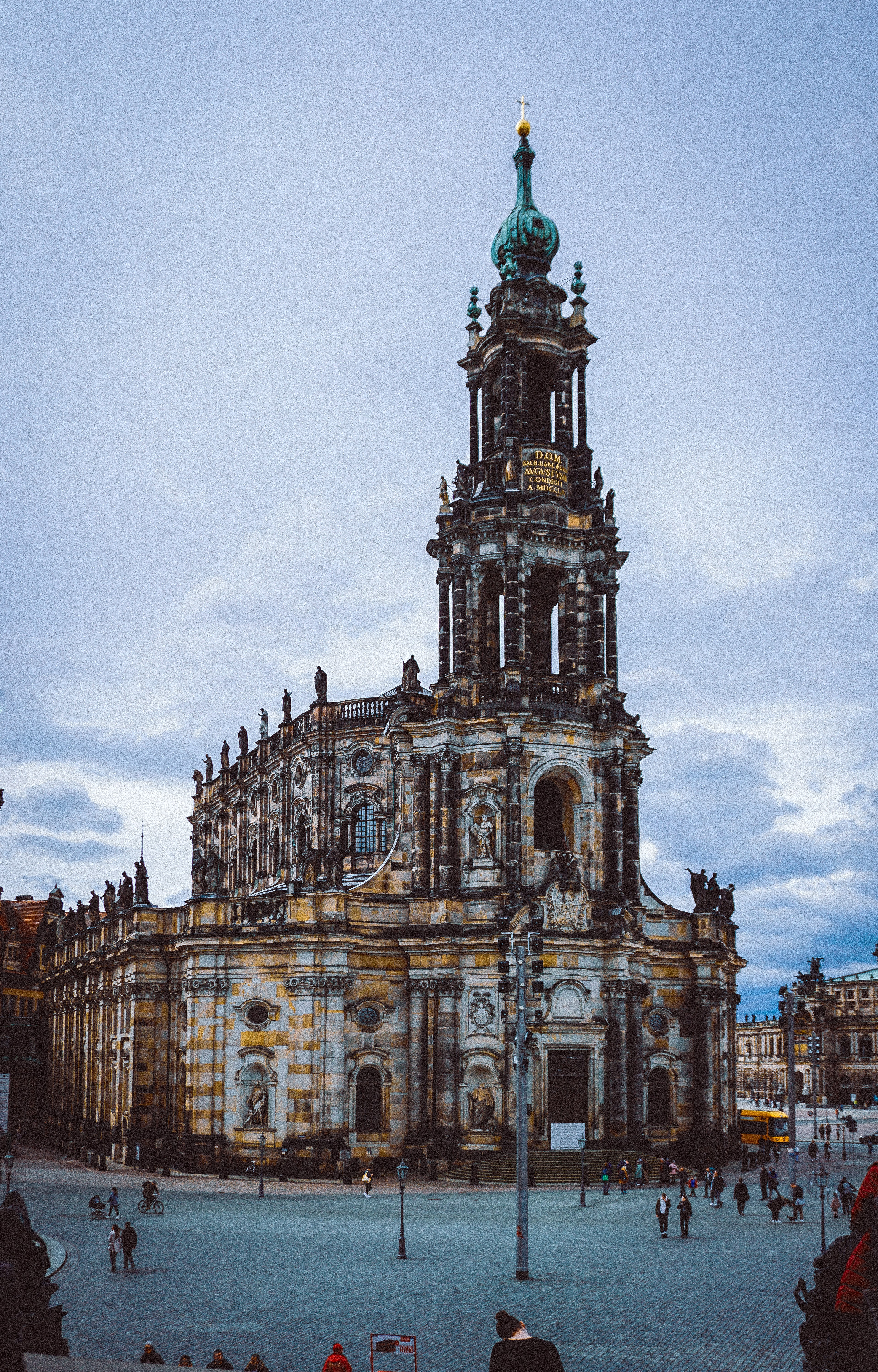 Baroque architecture of a grand church with intricate details and a striking tower, surrounded by a bustling square.