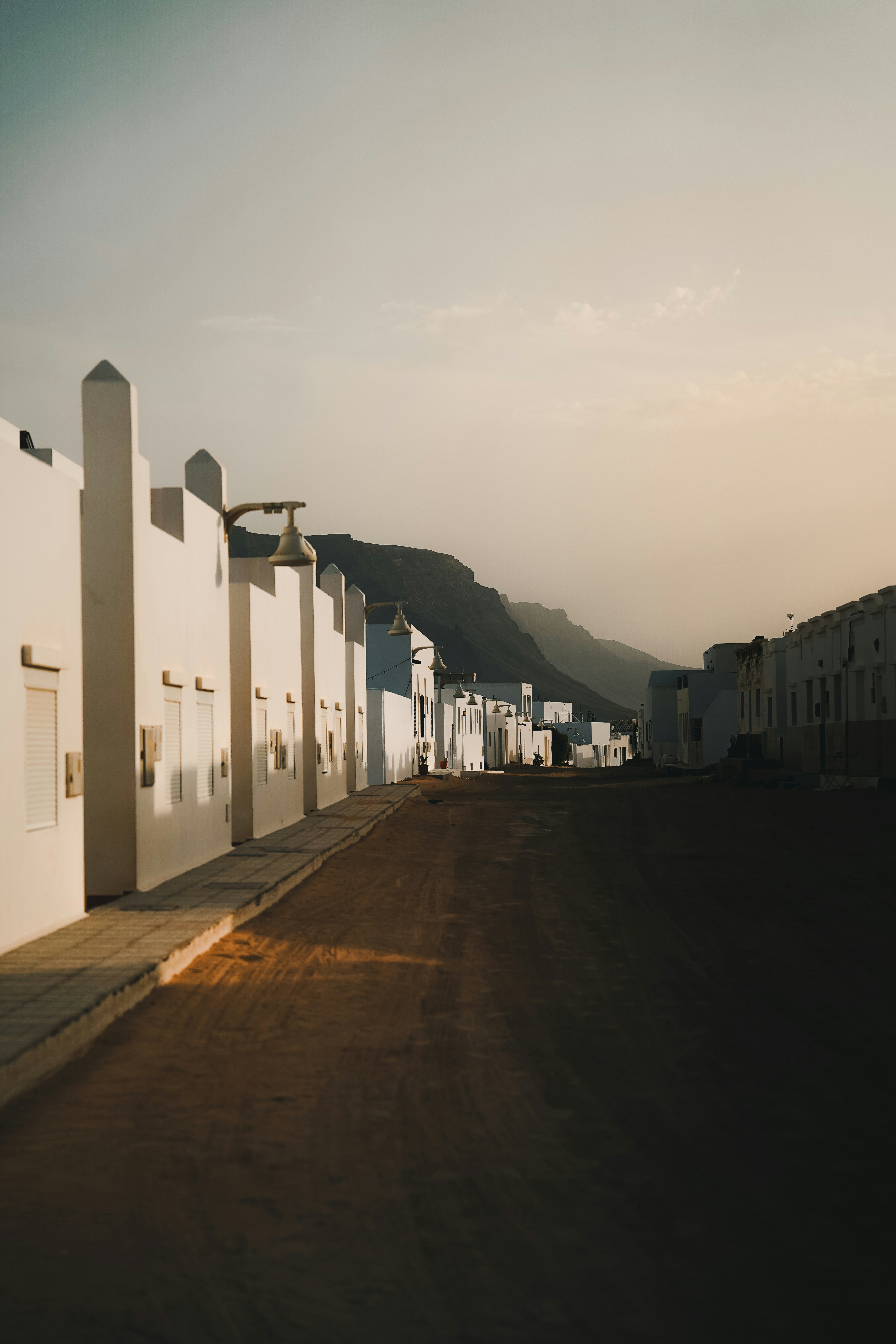Golden Hour Vein: White-Walled Desert Street Toward Distant Peaks