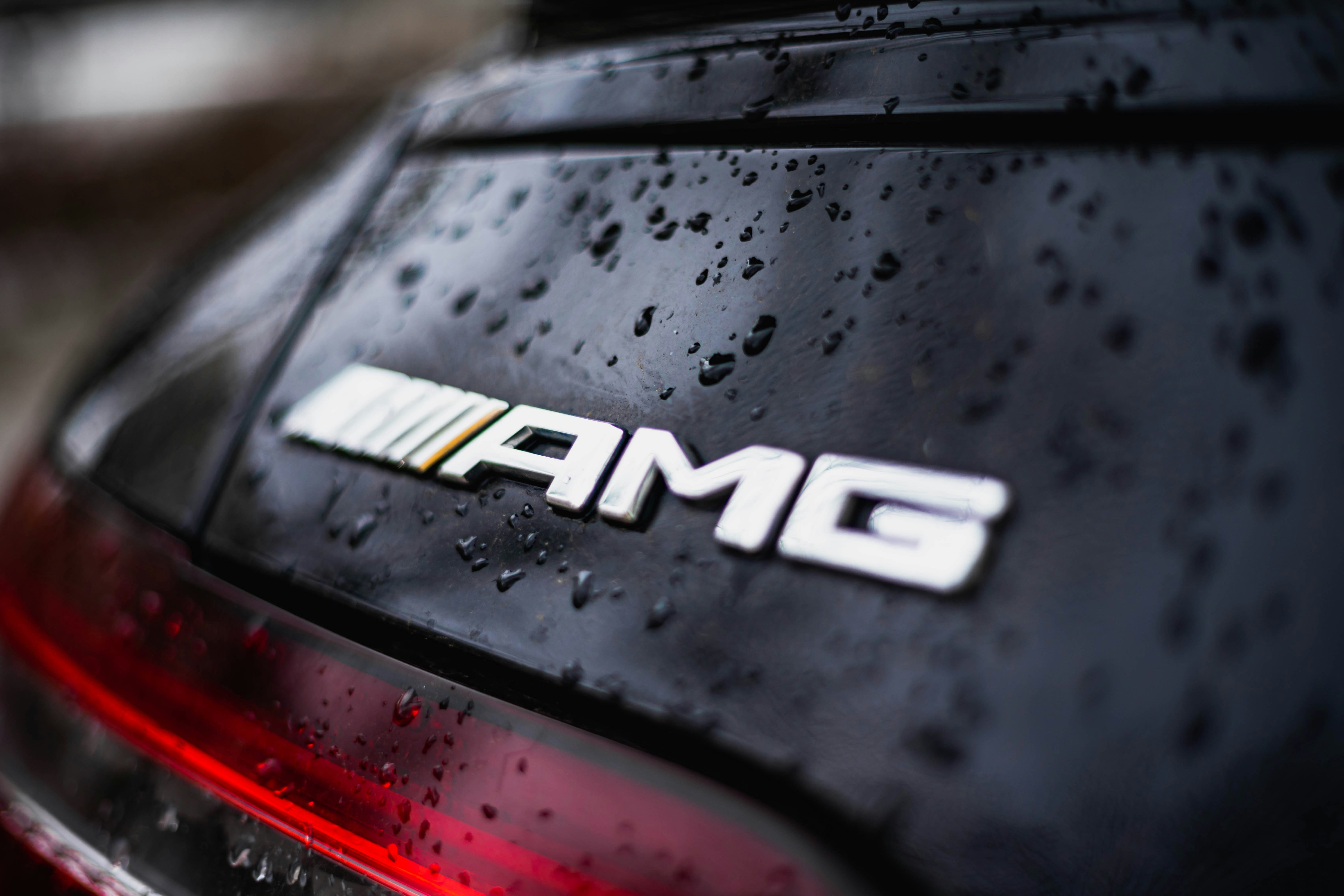 Close-up of a car's AMG emblem on a rain-speckled black surface.