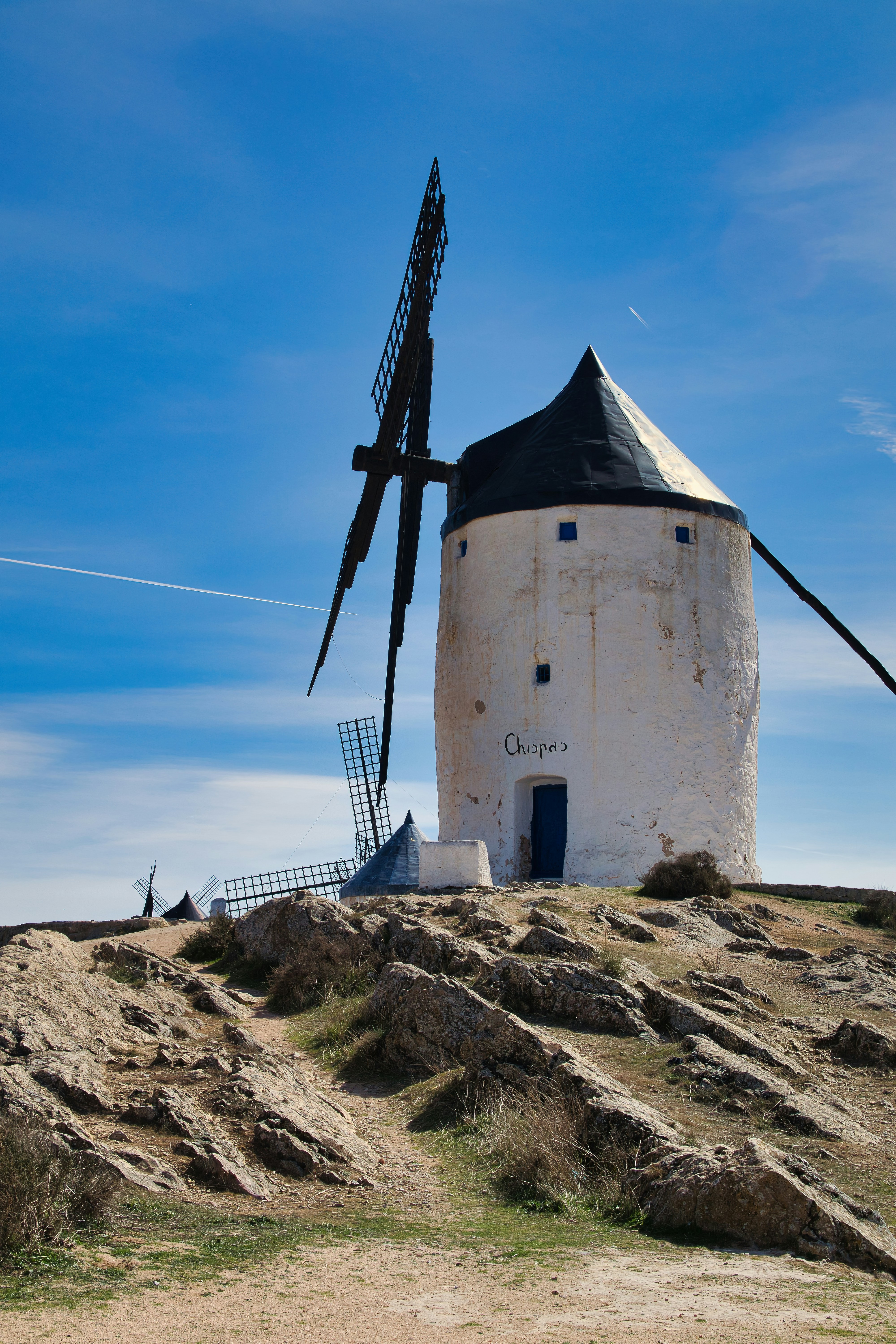 Historic windmill perched on rocky terrain under a clear blue sky, showcasing its iconic silhouette and structural details.