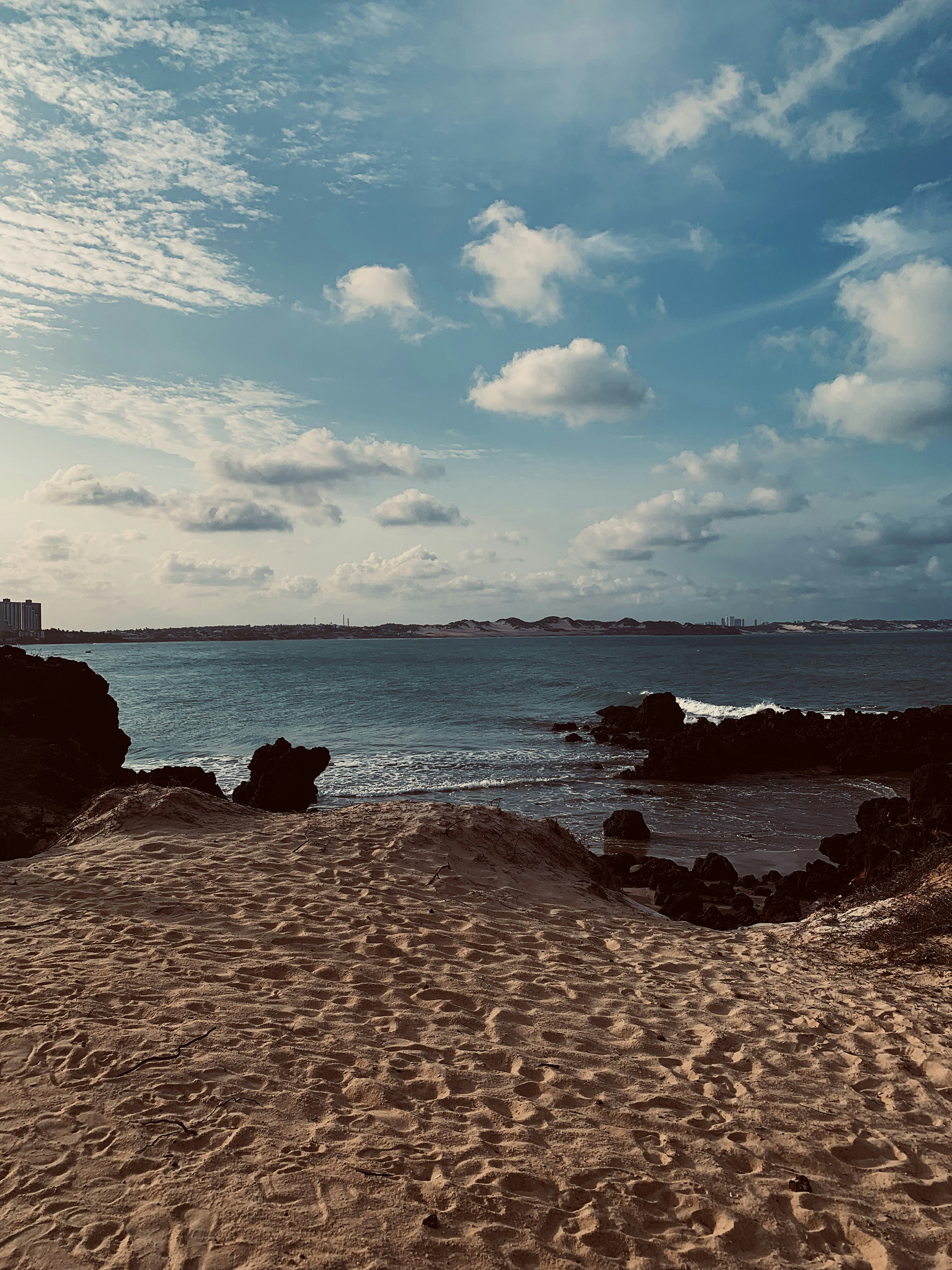 Sandy beach with rocky formations leading to a calm sea under a sky filled with clouds.