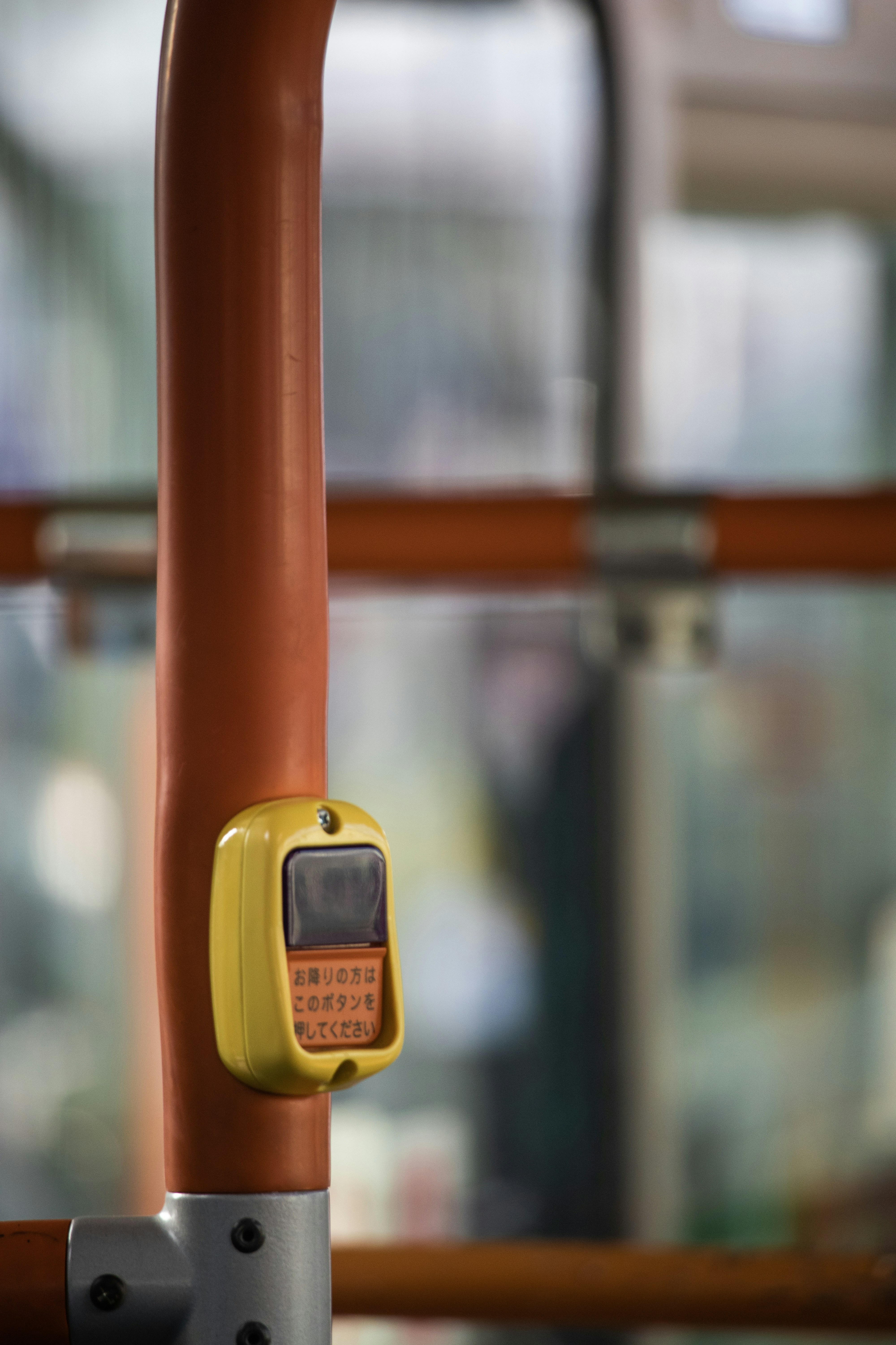 Transit Detail: Yellow Button on a Rust-Orange Handrail in Soft Bus Interior