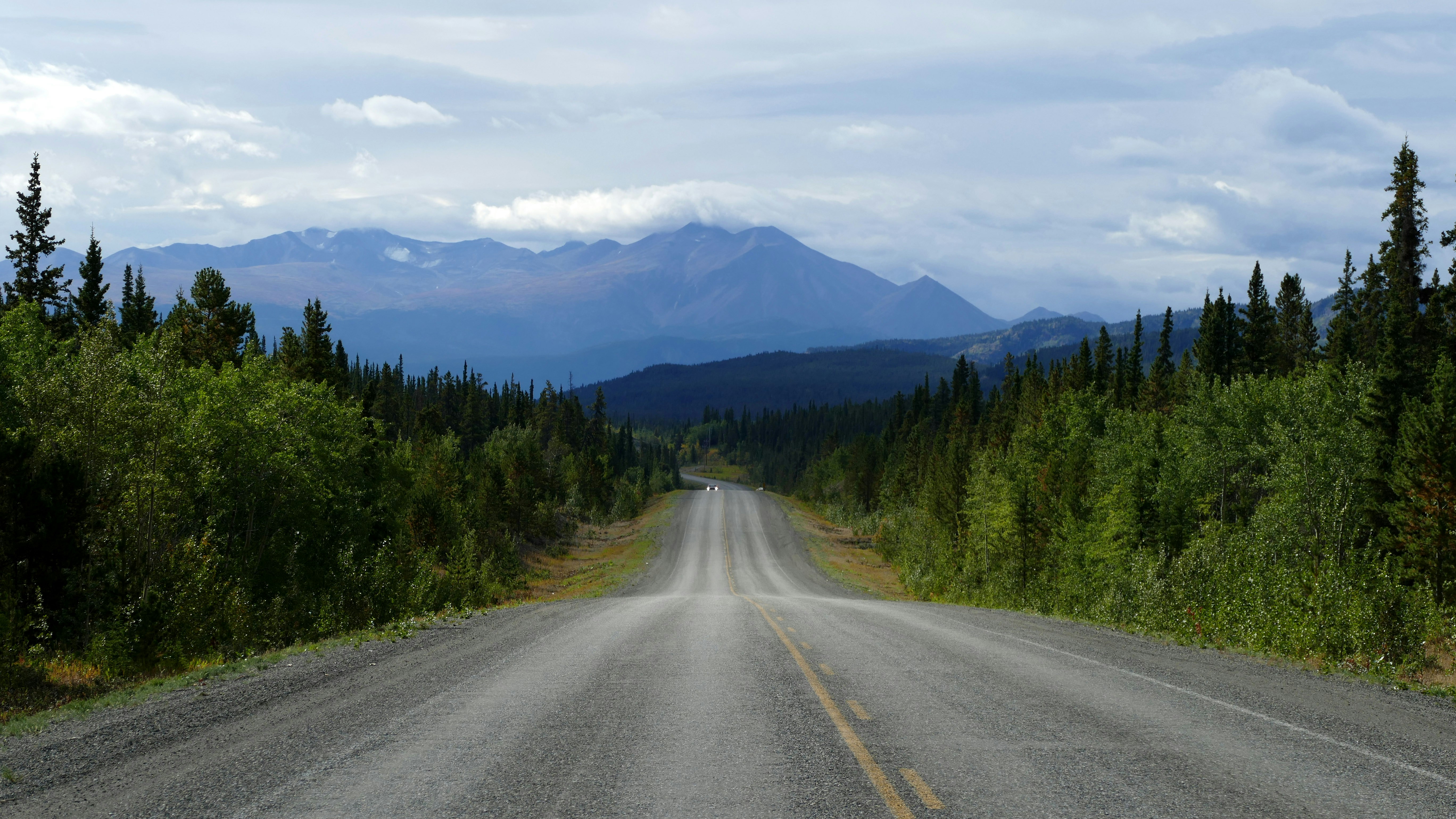 Car on a lonely road in Alaska with a mountain range on the background.