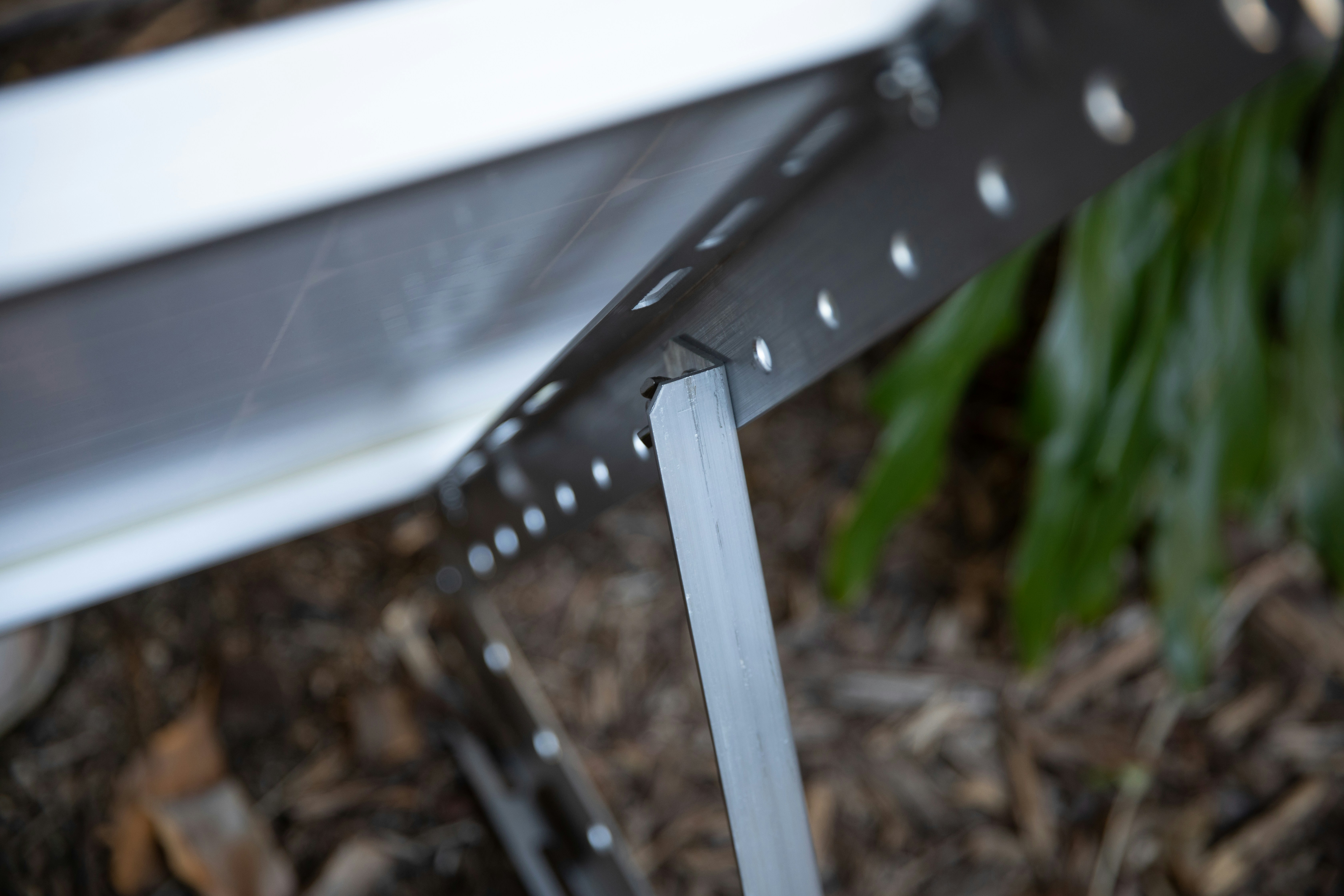 Rain-Kissed Perforated Rail: A Close-Up on Steel Edges and a Stabilizing Leg