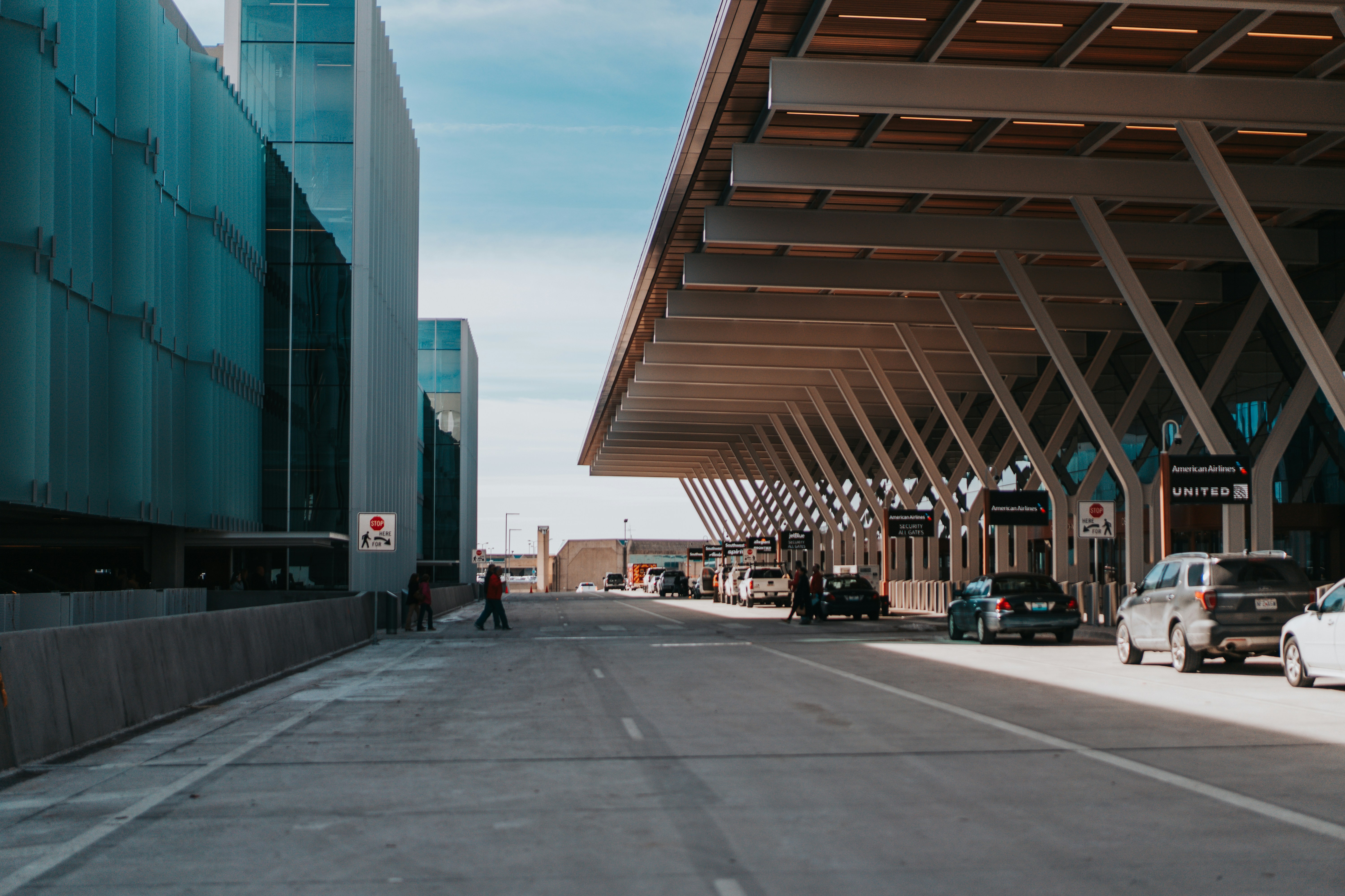 Contemporary airport terminal with angular architecture and parked vehicles under a clear sky.
