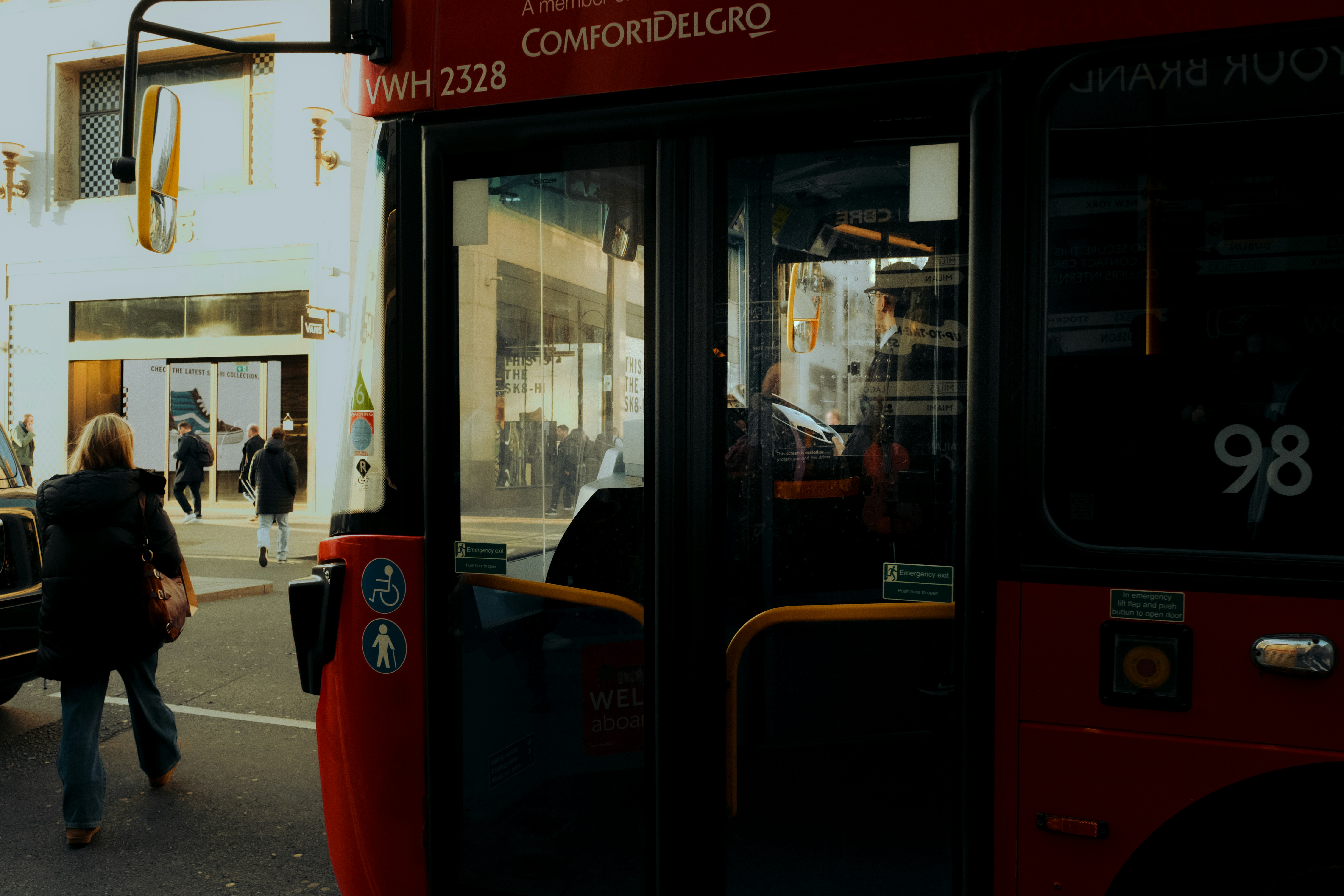 A red bus driving down a street next to a tall building photo – Free ...