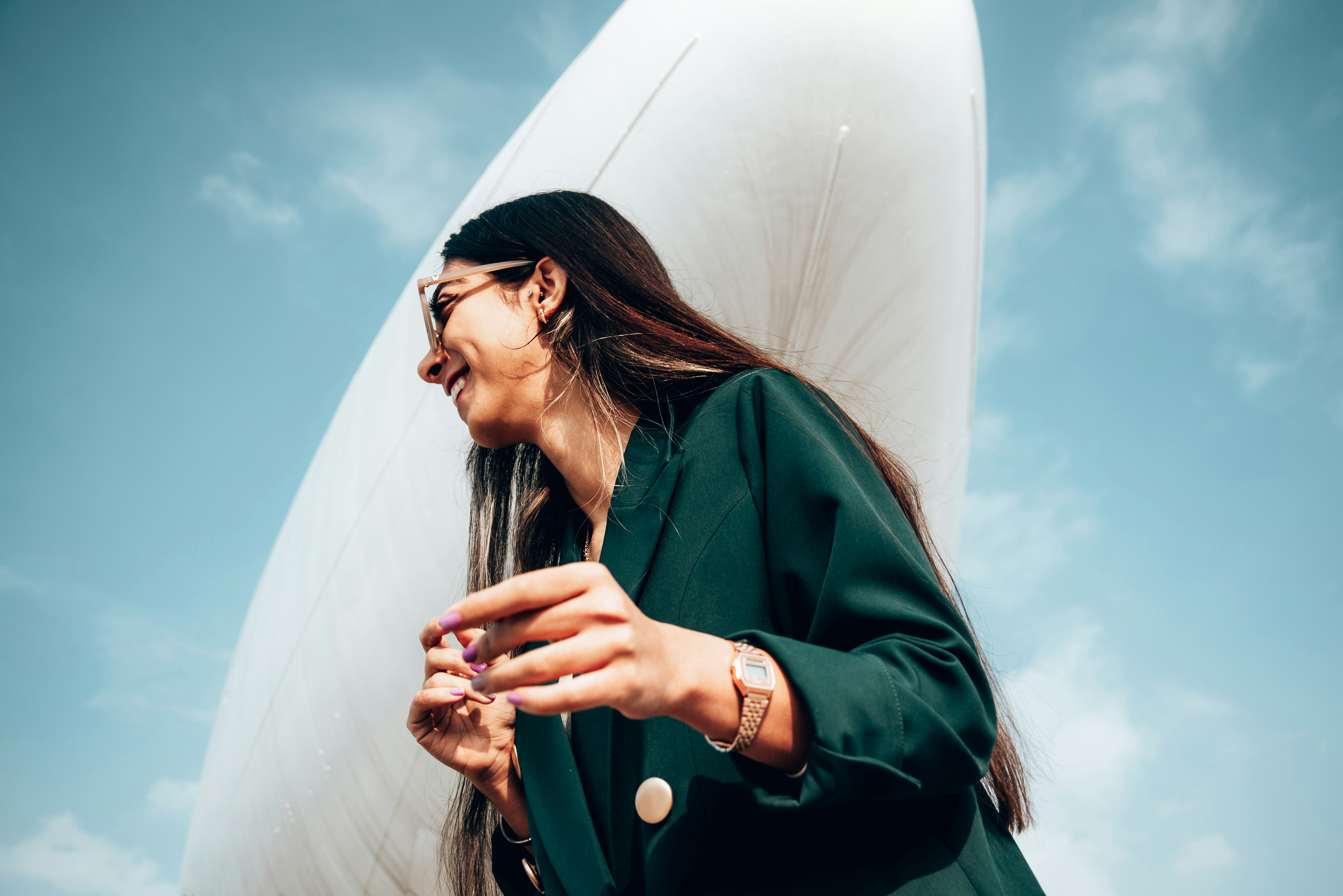 Green blazer under a towering surfboard: a low-angle portrait against a bright blue sky
