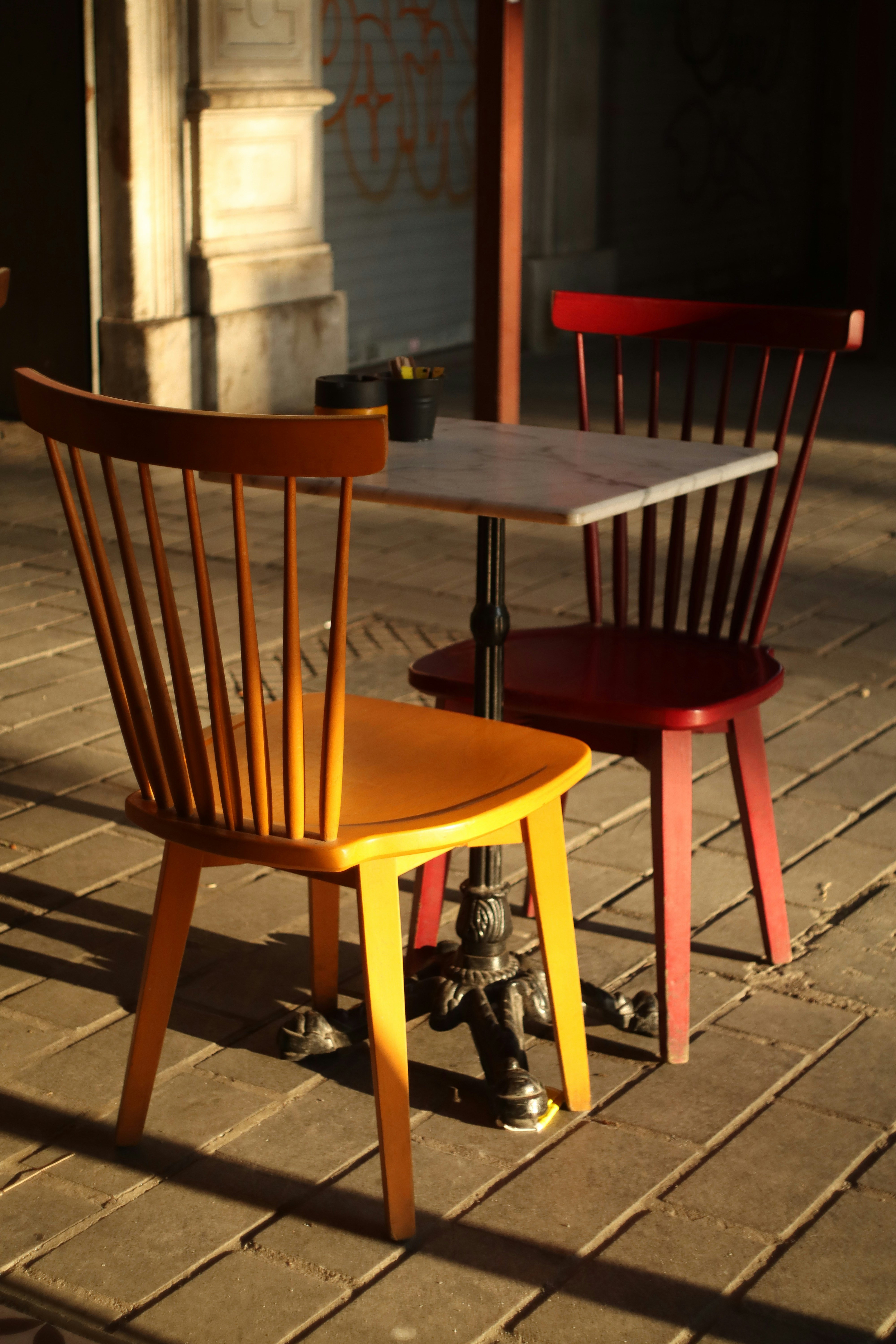 Sunlit Duet: Yellow and Crimson Chairs Framing a Marble Table