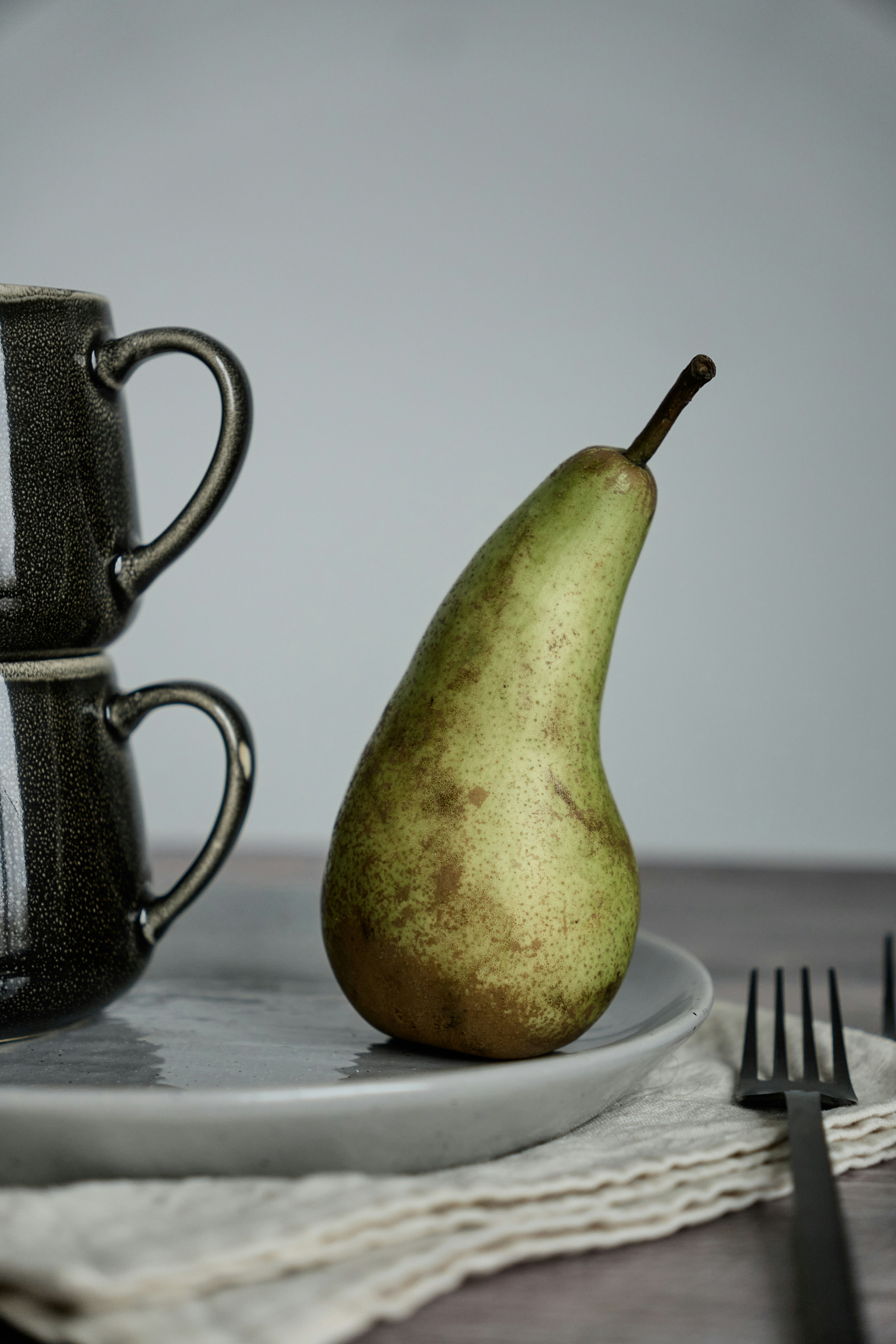 a pear sitting on a plate next to two cups