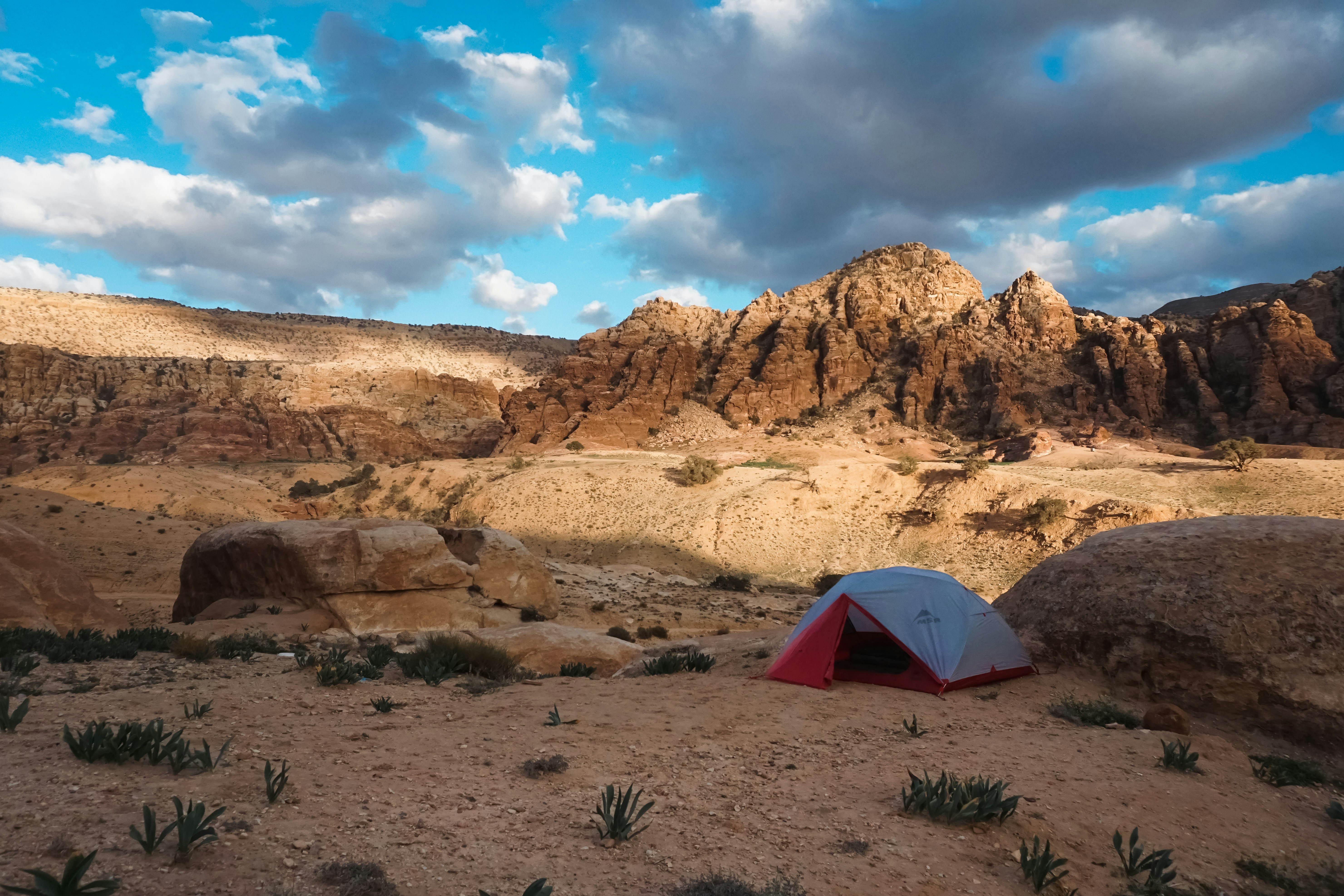 Red and gray tent nestled in a rugged desert landscape under a dramatic sky. The scene captures the essence of outdoor adventure.