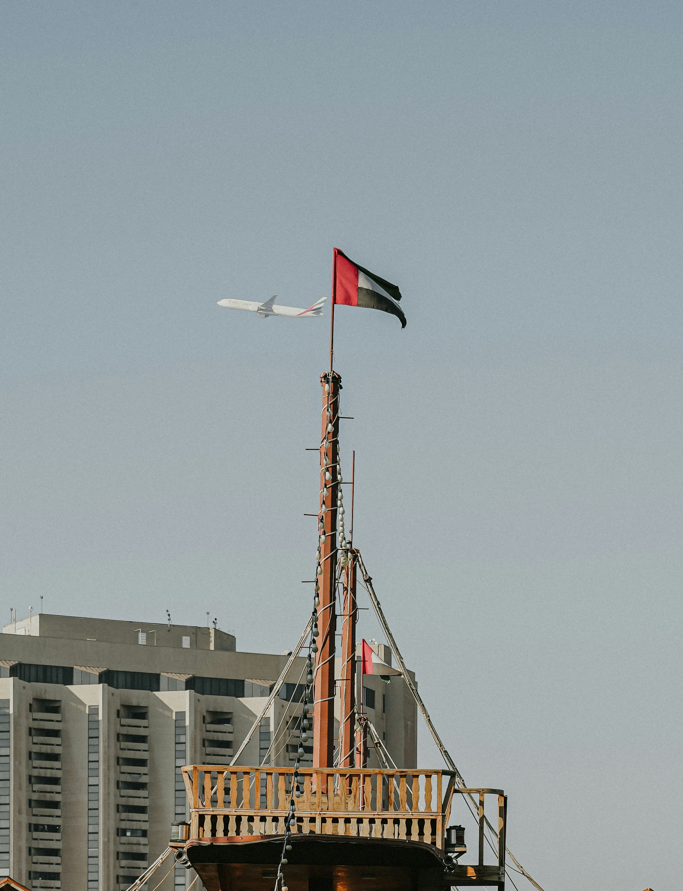 Flag-Topped Mast Framed by Sky, with a Jet in the Distance