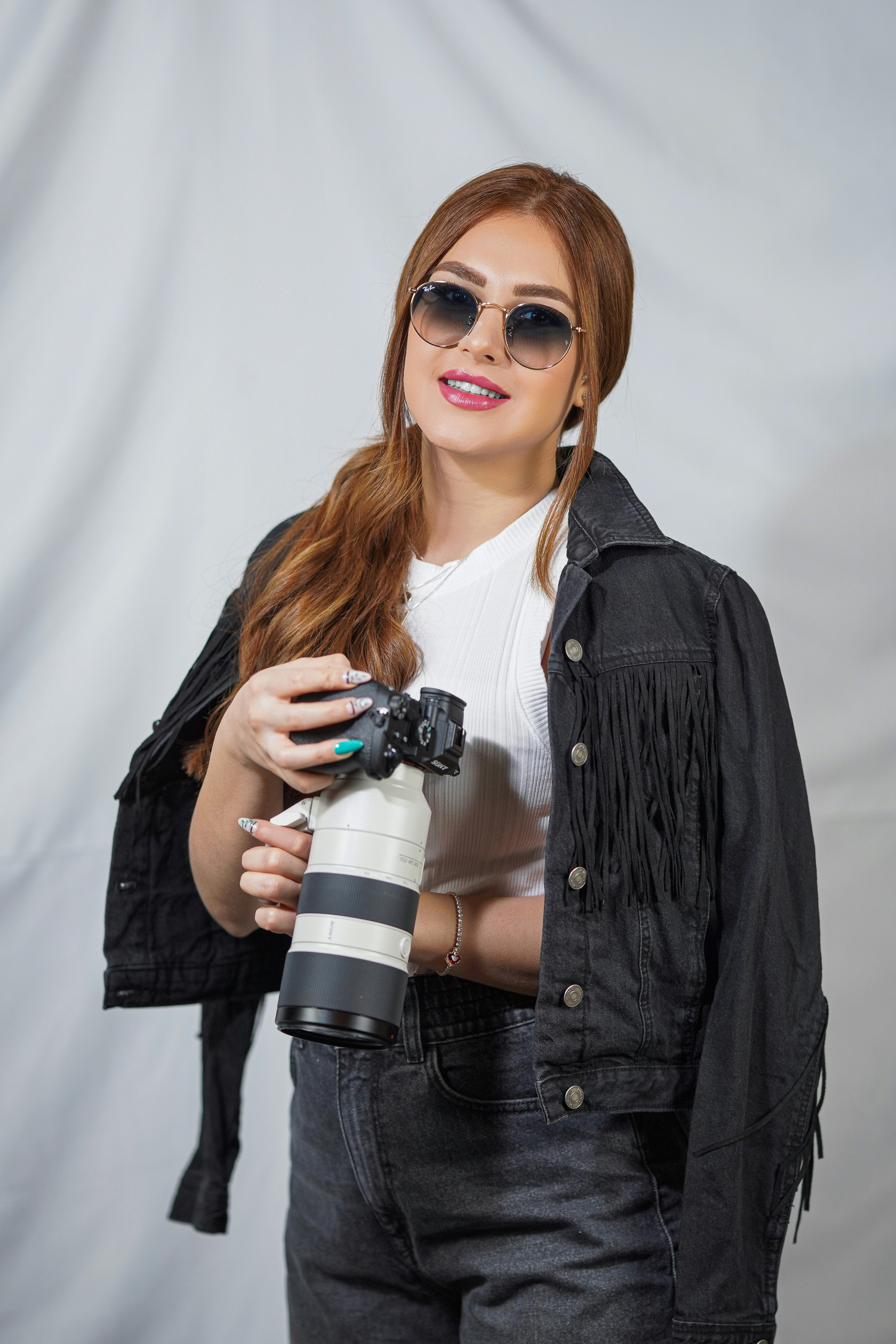 Portrait of a confident photographer with a white telephoto lens against a neutral studio backdrop