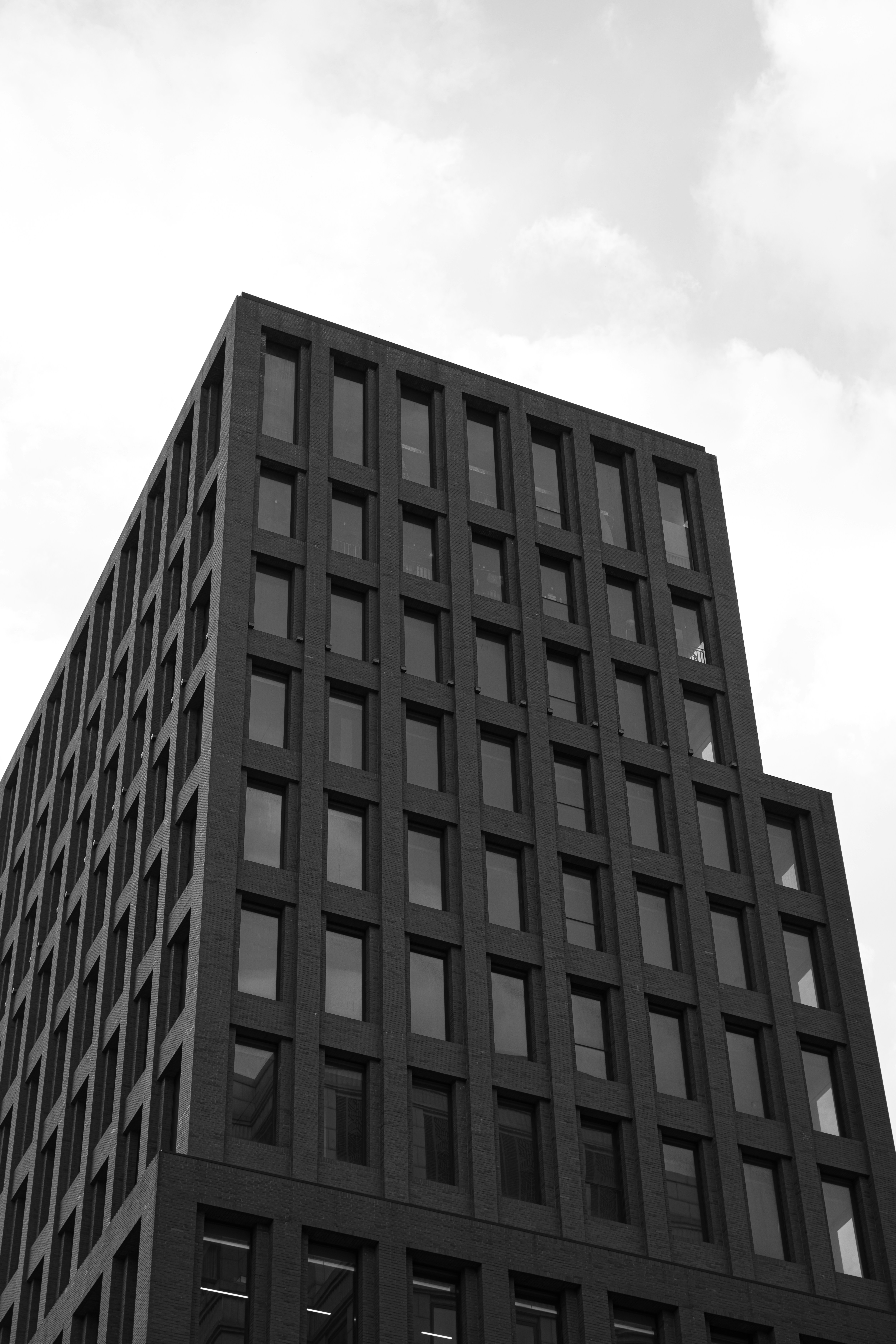 Modern architectural structure with a geometric facade and a grid of windows, captured in black and white. The image emphasizes the interplay of light and shadow on the building's surfaces.